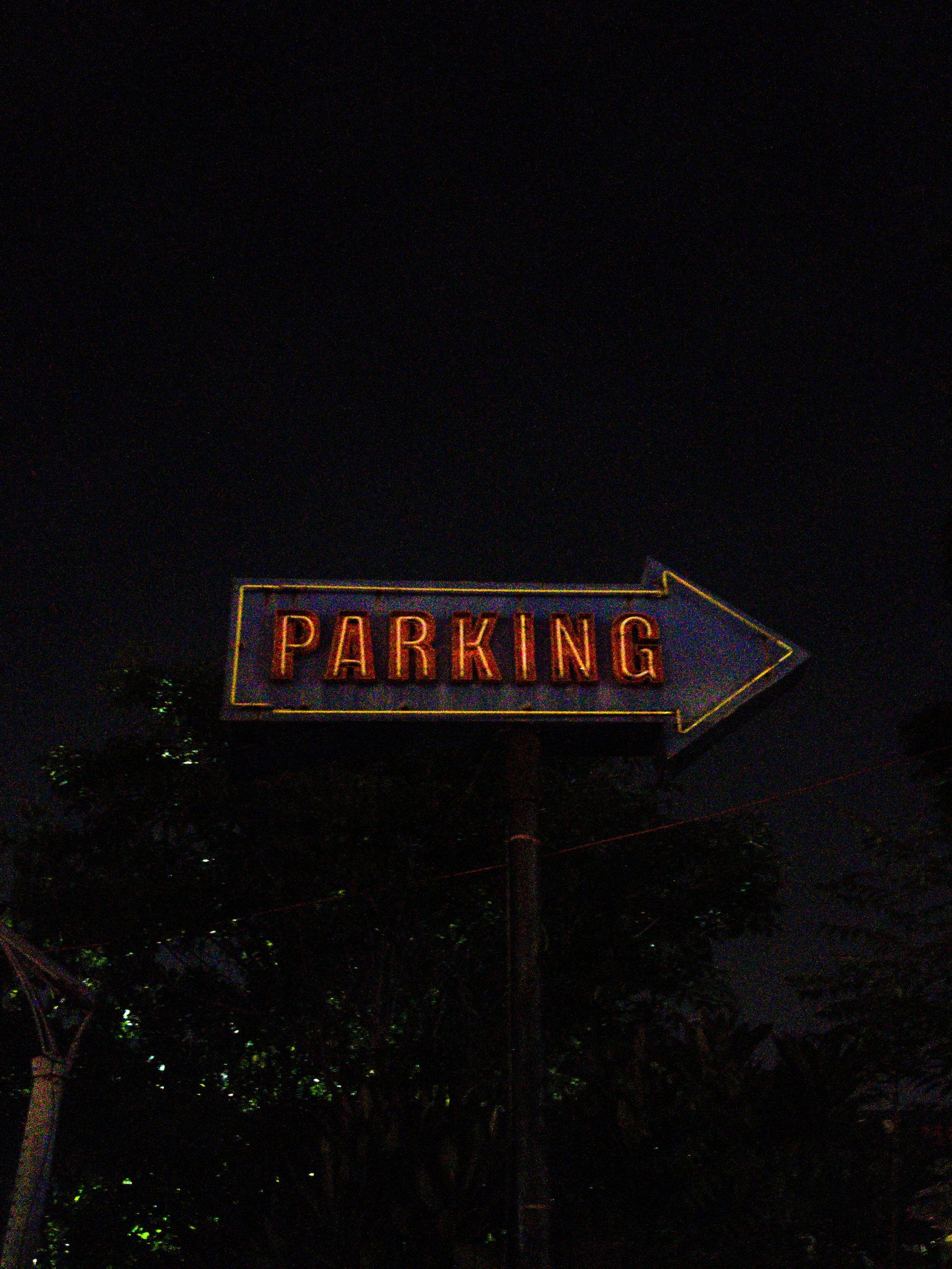 Neon-lit parking sign on a dark street, arrow pointing right; photograph.