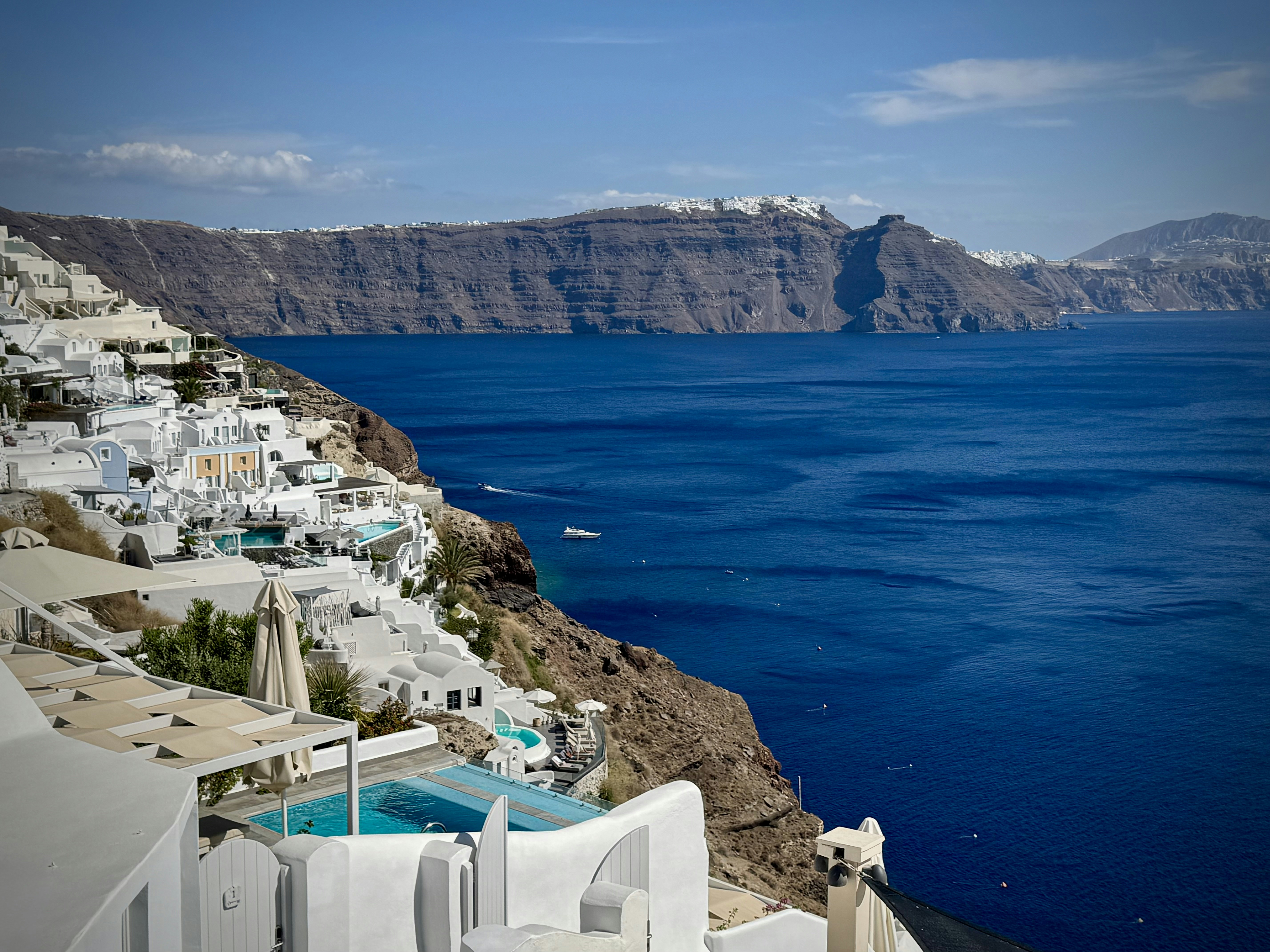 Whitewashed buildings on a cliffside overlooking the deep blue Aegean Sea under a clear sky.