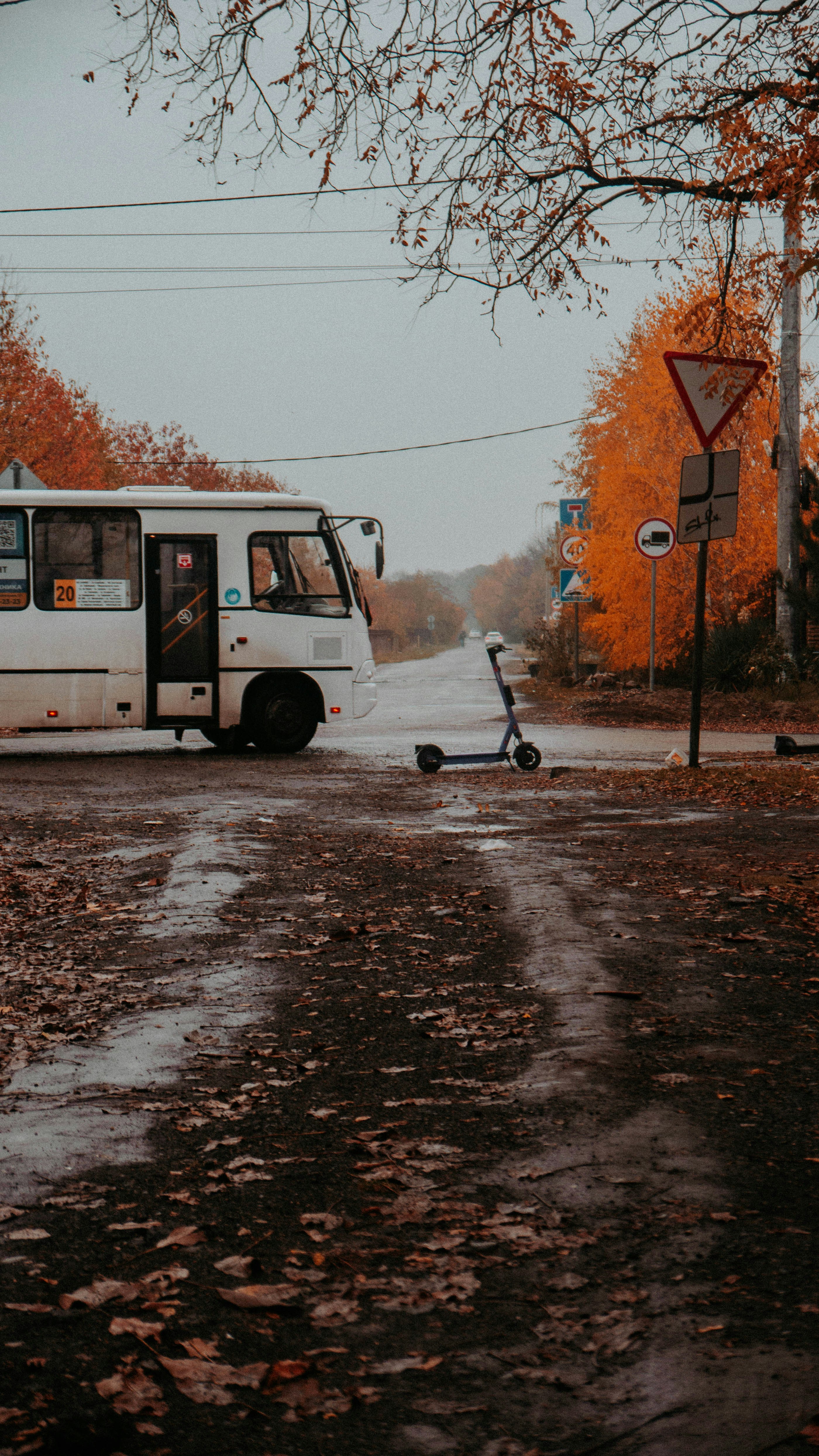 Crossroads of Fall: A White Bus, a Scooter, and Autumn's Quiet Street