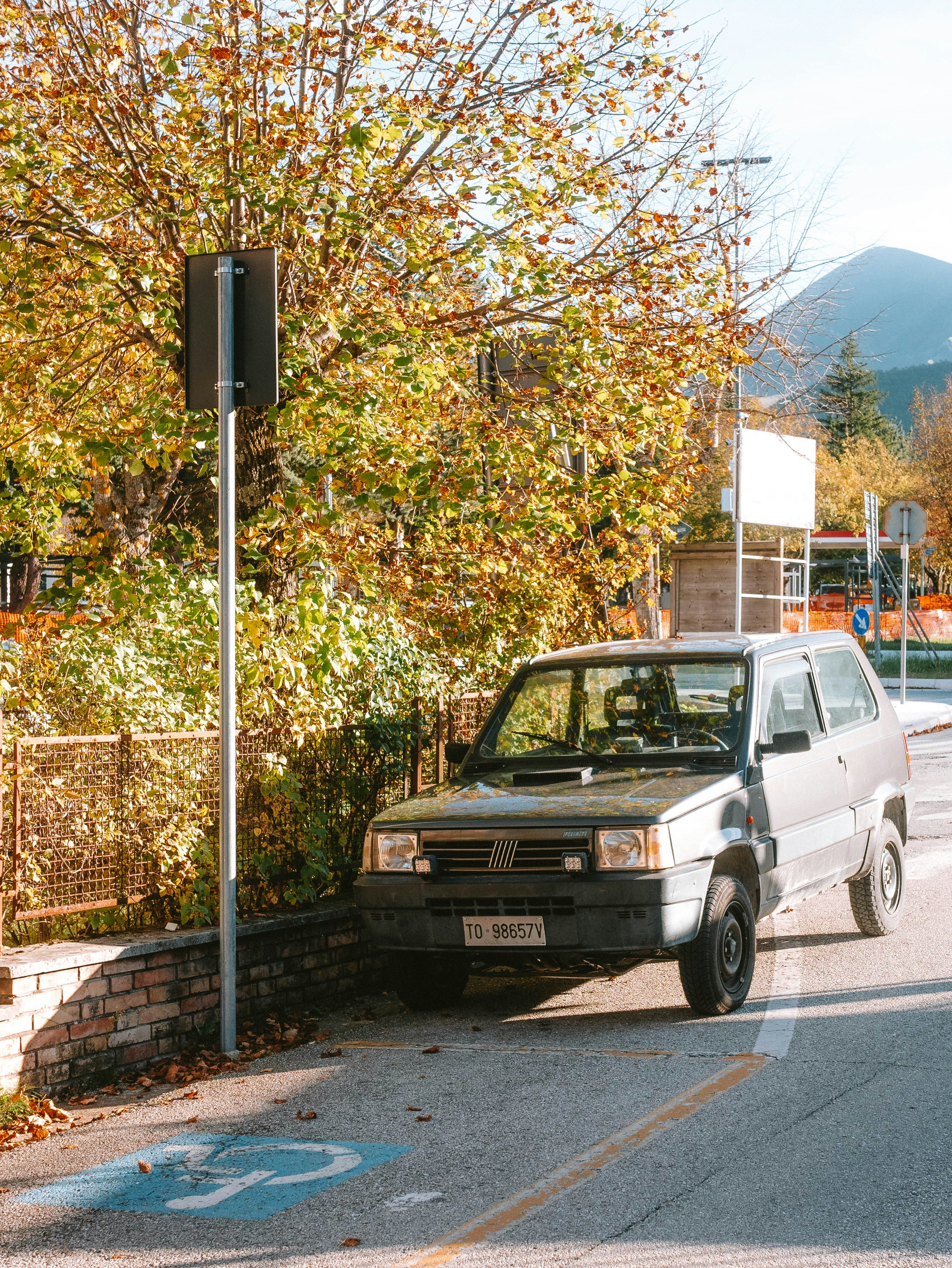 Gold-Leaf Street: A Compact Van Paused Under Autumn Trees