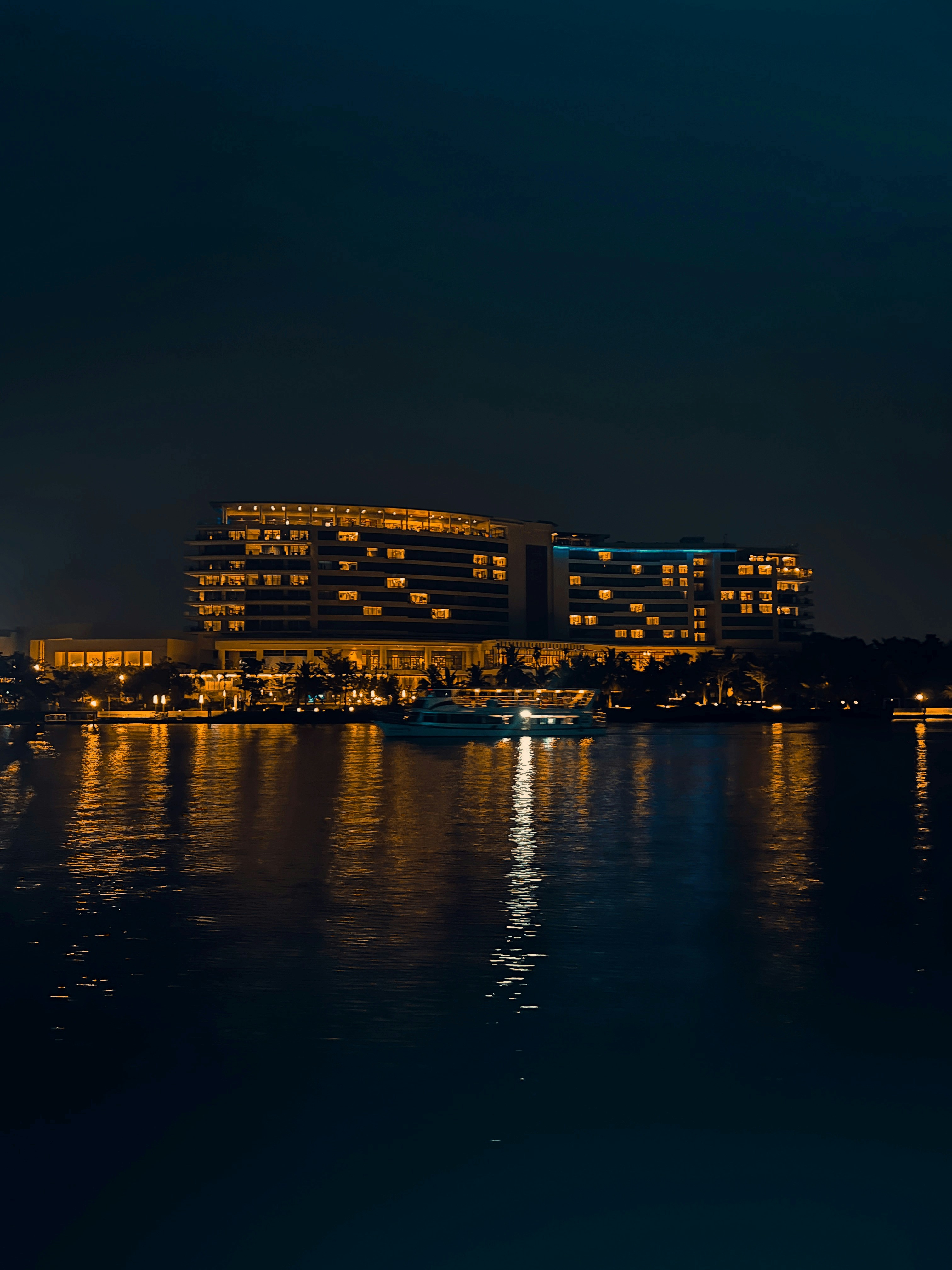 Illuminated modern hotel by the water, reflecting softly in the calm night. The scene captures a tranquil urban atmosphere.