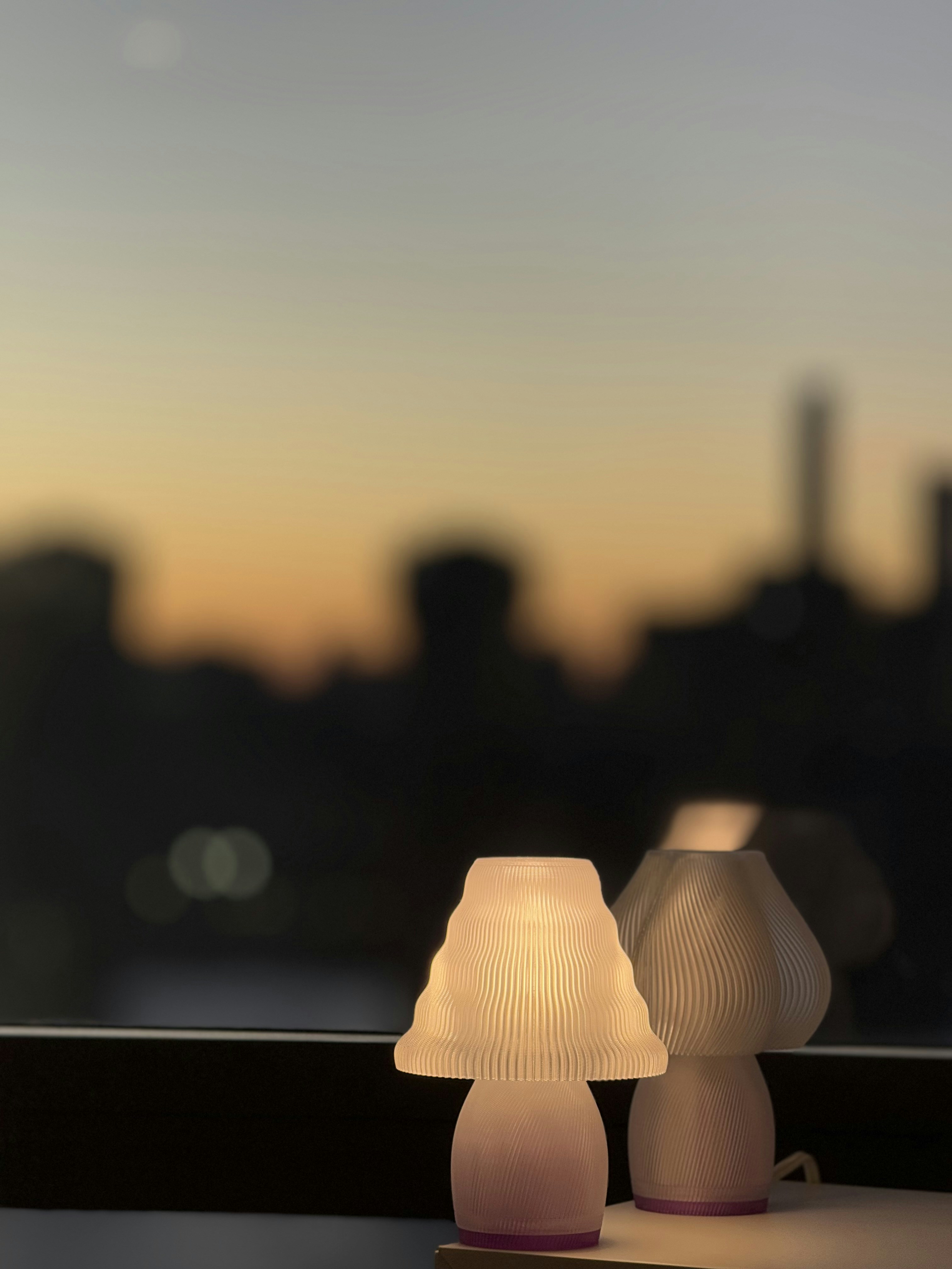 Softly glowing lamps in the foreground with a blurred city skyline at sunset in the background.