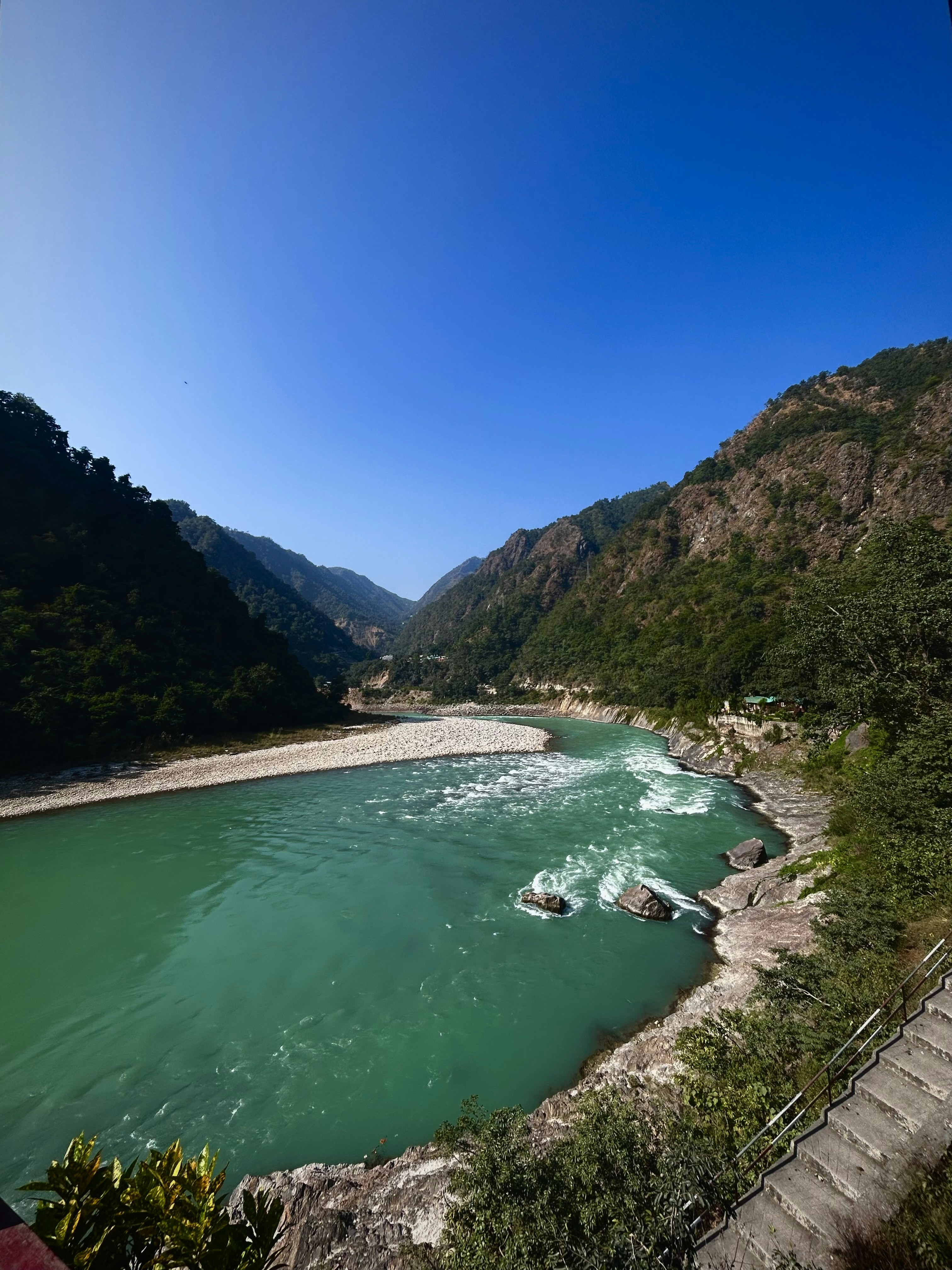 Turquoise river meandering through lush green mountains under a clear blue sky, showcasing a tranquil natural landscape.