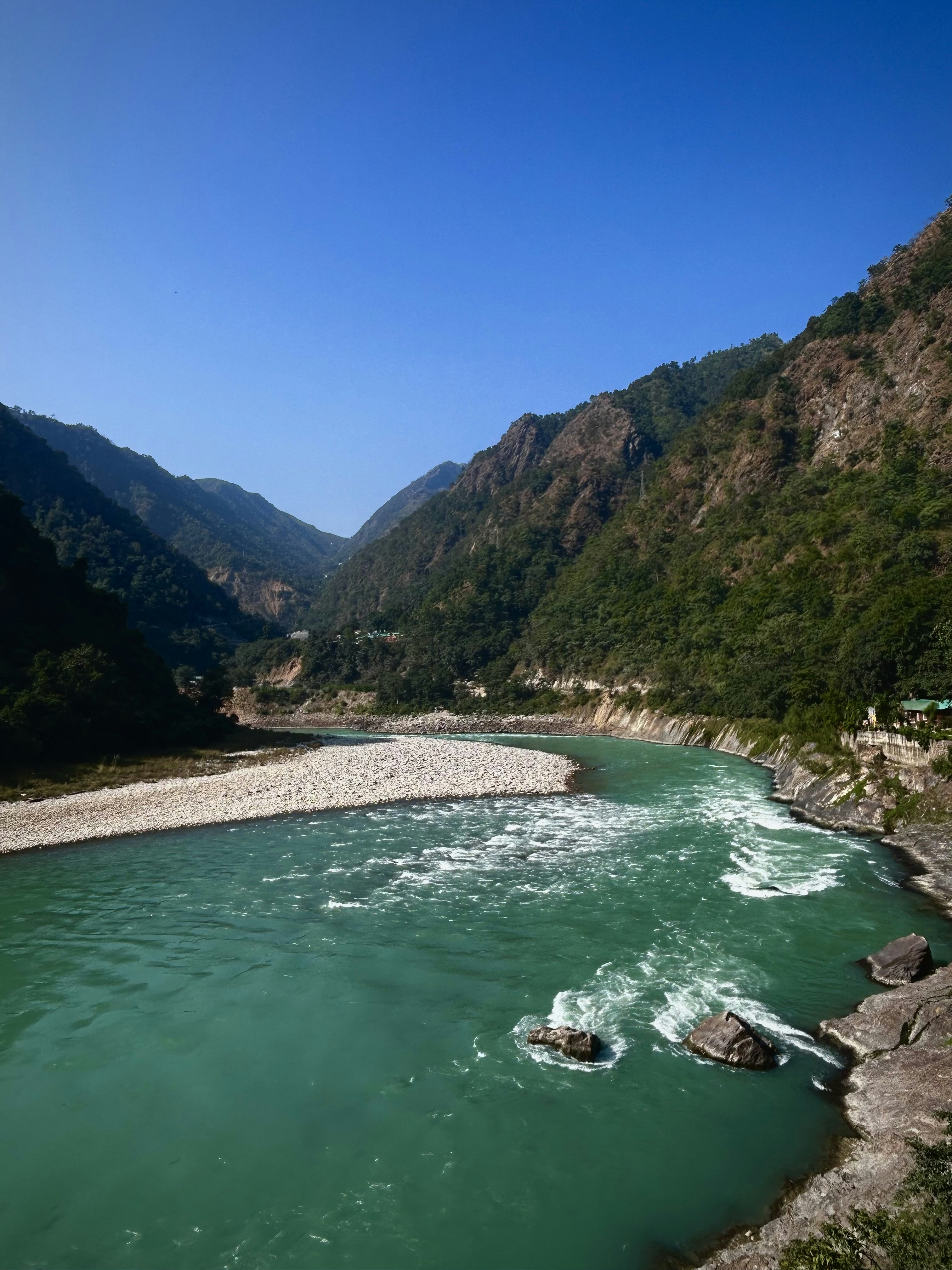 Turquoise river winding through a lush valley flanked by towering mountains under a clear blue sky.