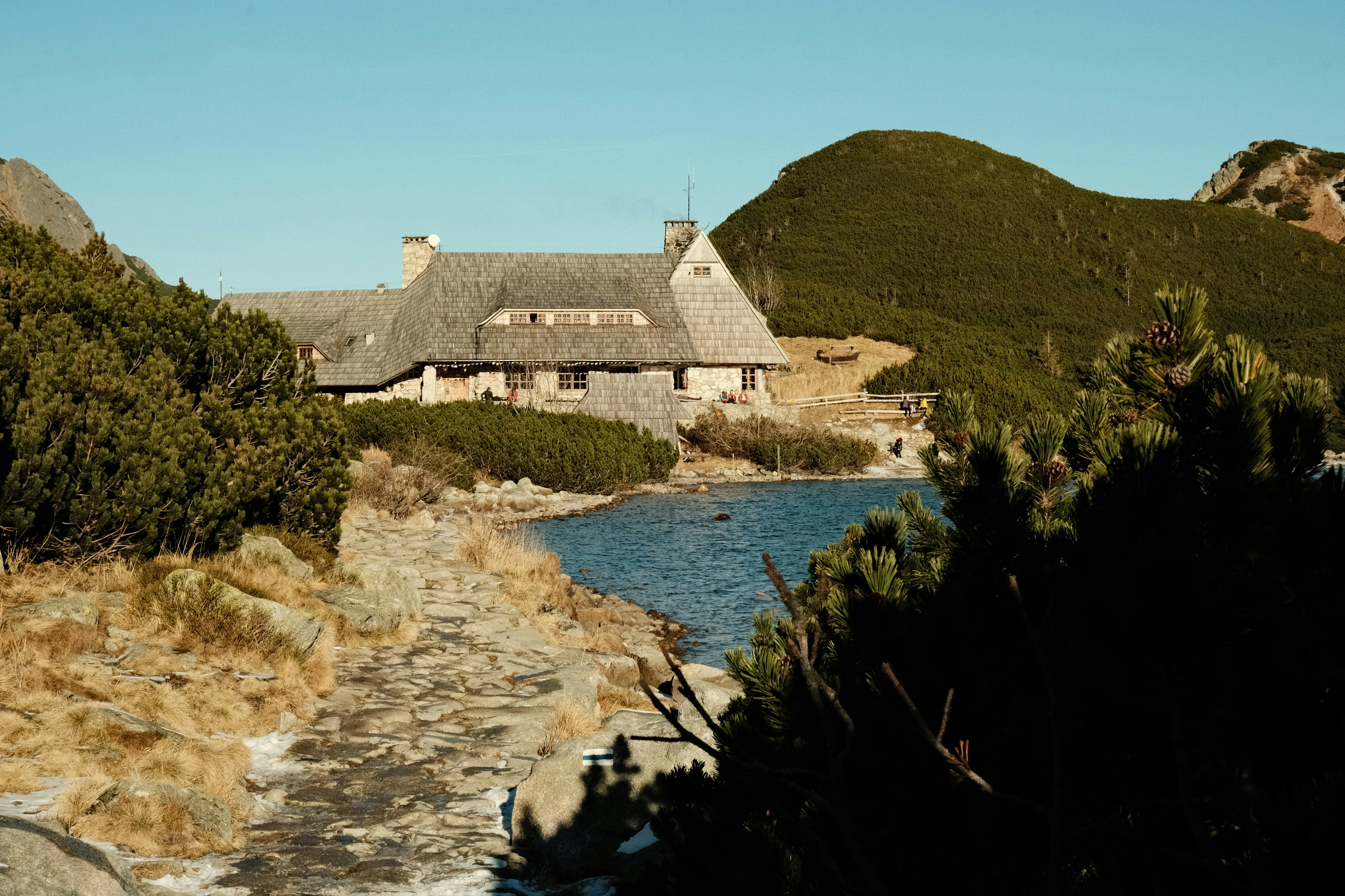 Chalet nestled on a hill beside a tranquil lake under a clear blue sky.