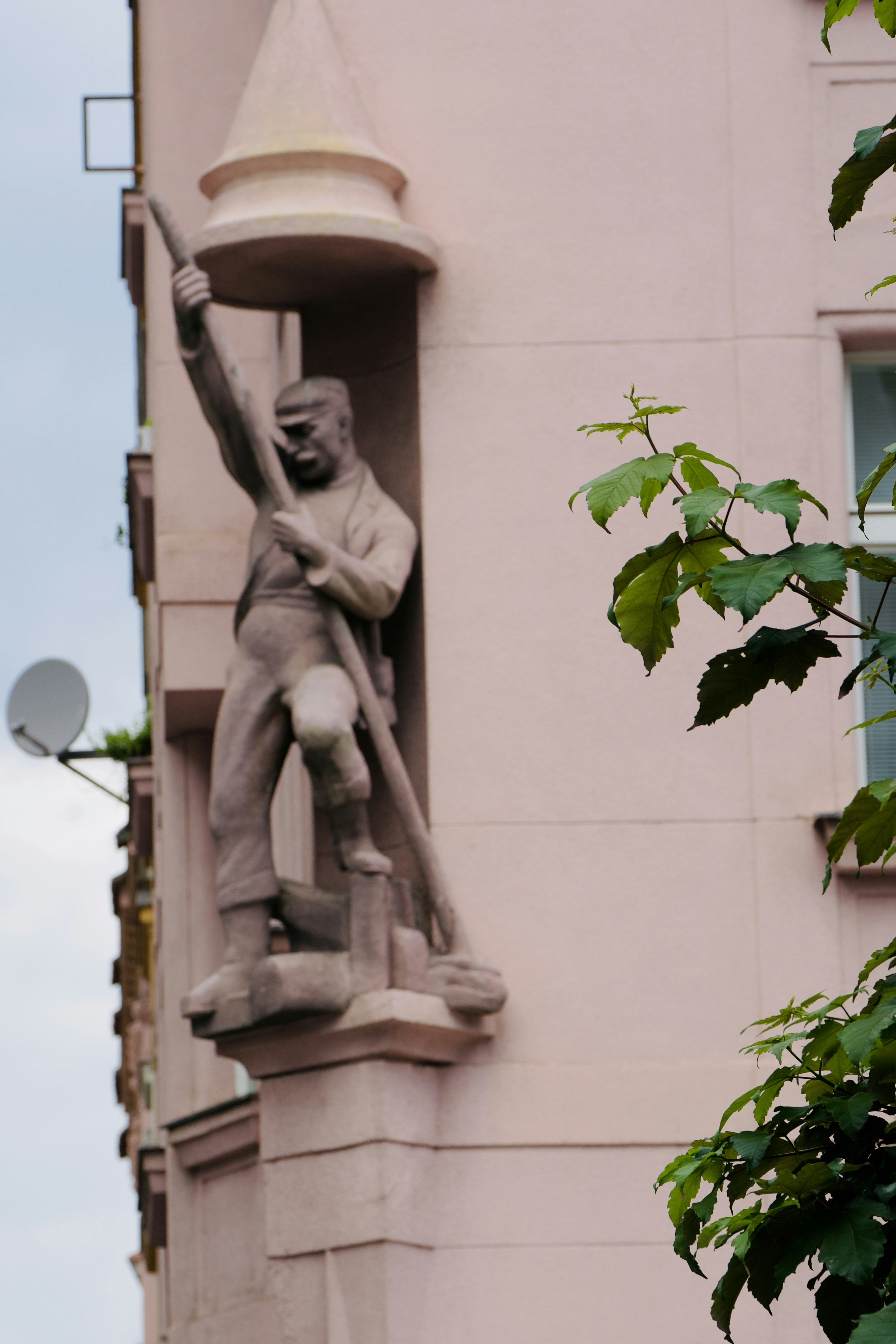 Corner Sentinel: Stone Figure Reaching from a Pale Pink Facade