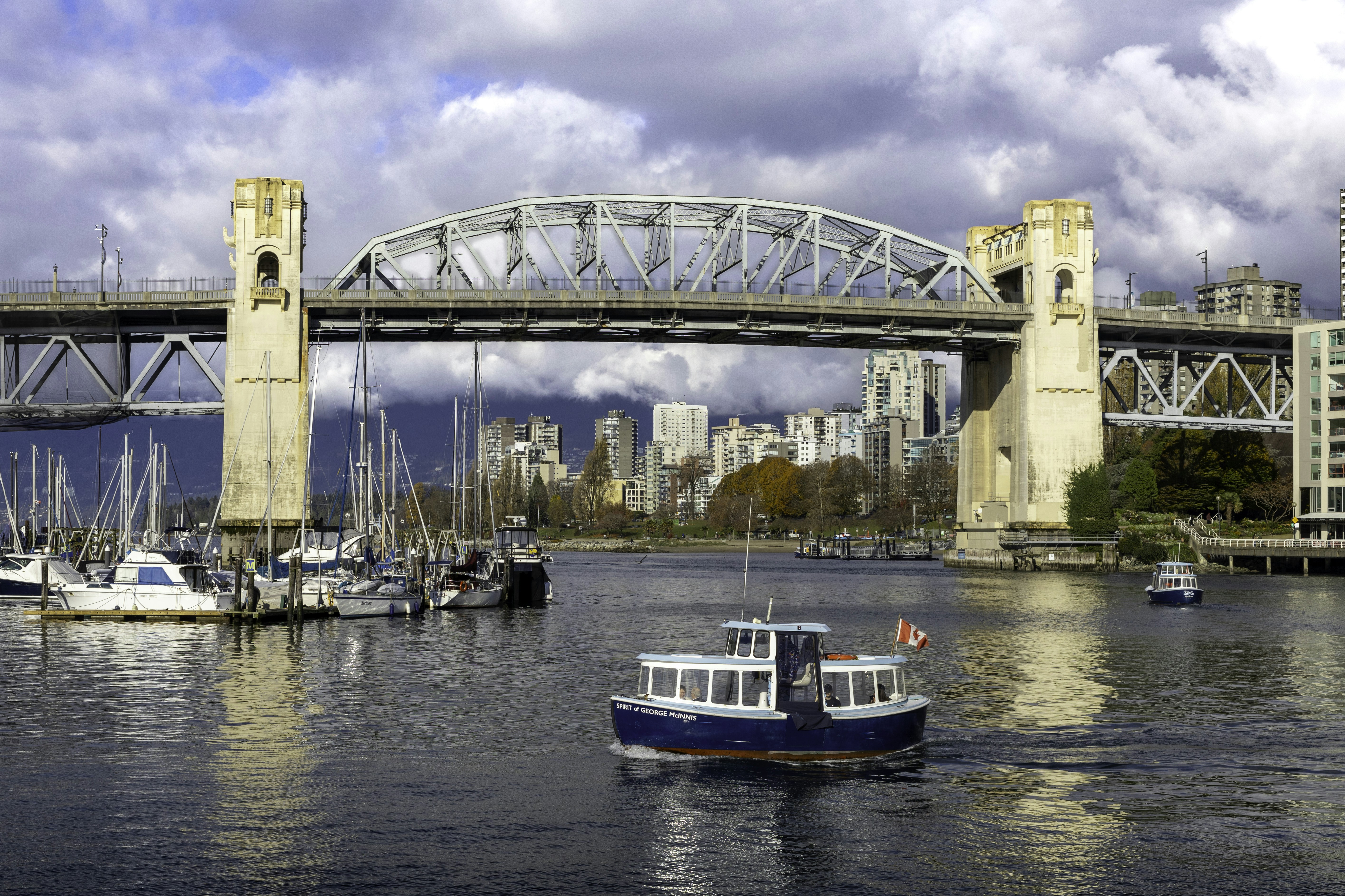 Small boat navigating calm waters with a towering bridge and city skyline in the background.