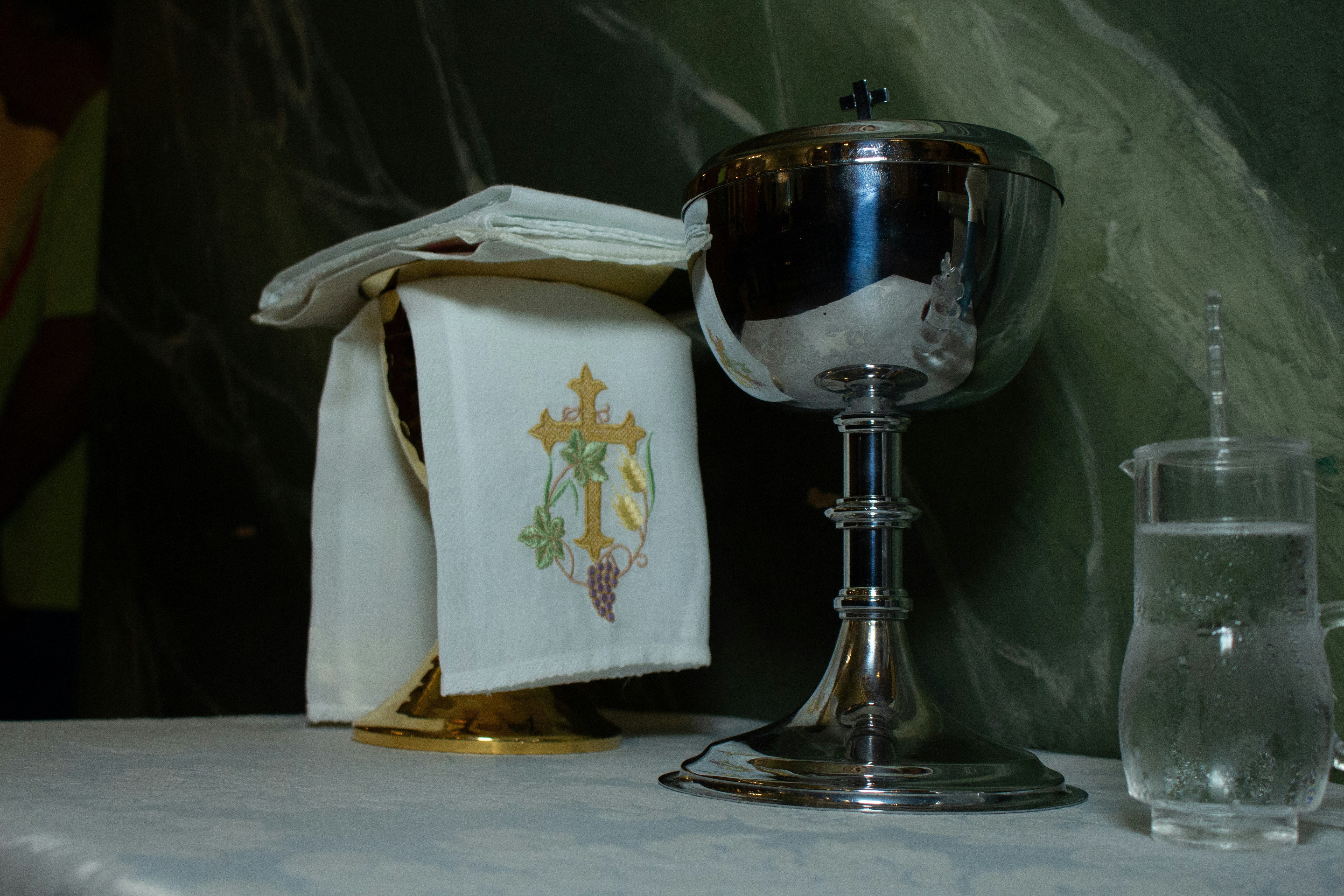 Chalice on a Quiet Altar: Silver Vessel with Crest-Woven Cloth and Glass Bottle