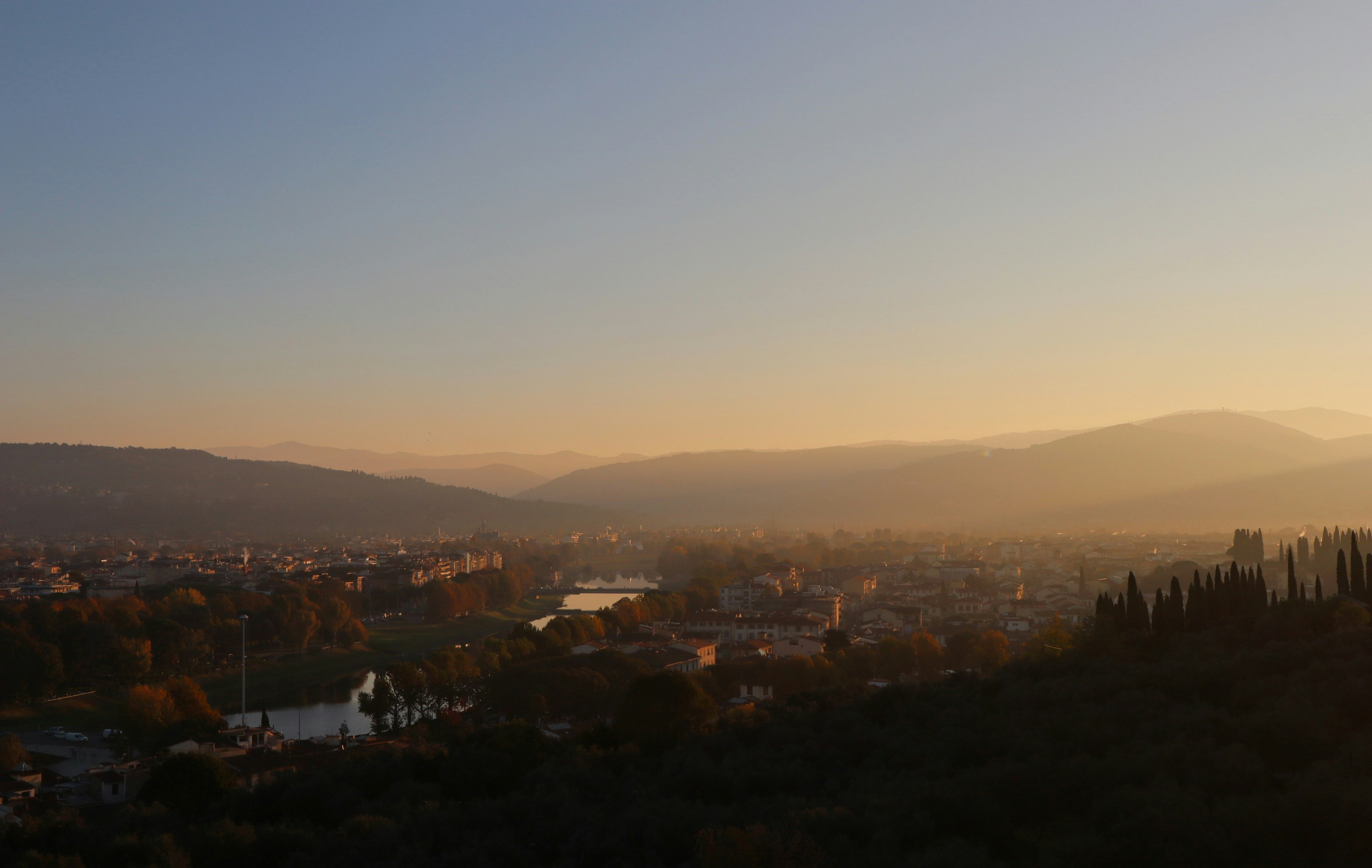 Golden sunset casting a warm glow over a serene valley, highlighting the interplay of light and shadow across the landscape.