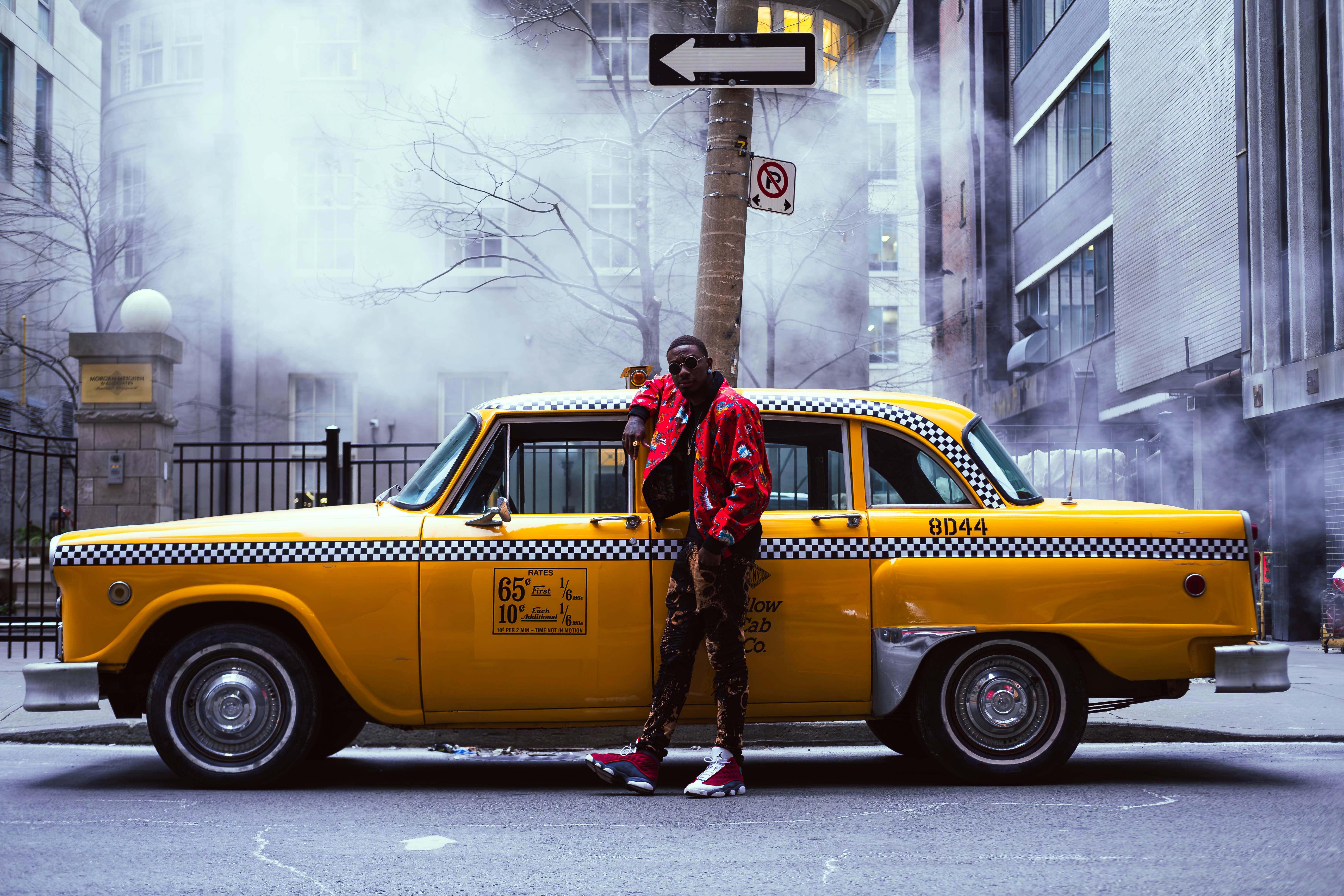 A man standing next to a yellow taxi on a city street photo – Free ...