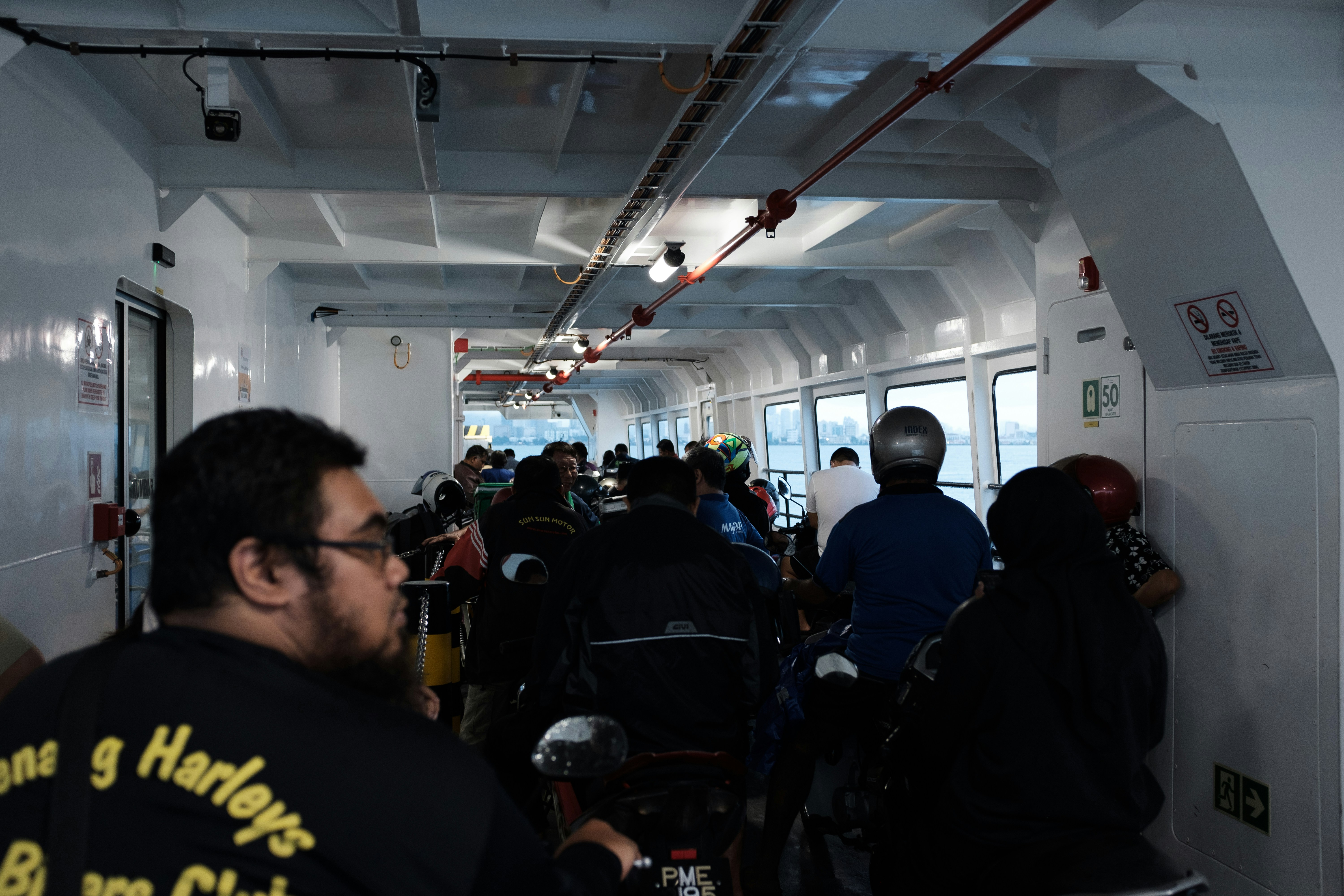 Motorcyclists gathered in a ferry's interior, under fluorescent lighting, awaiting transit.