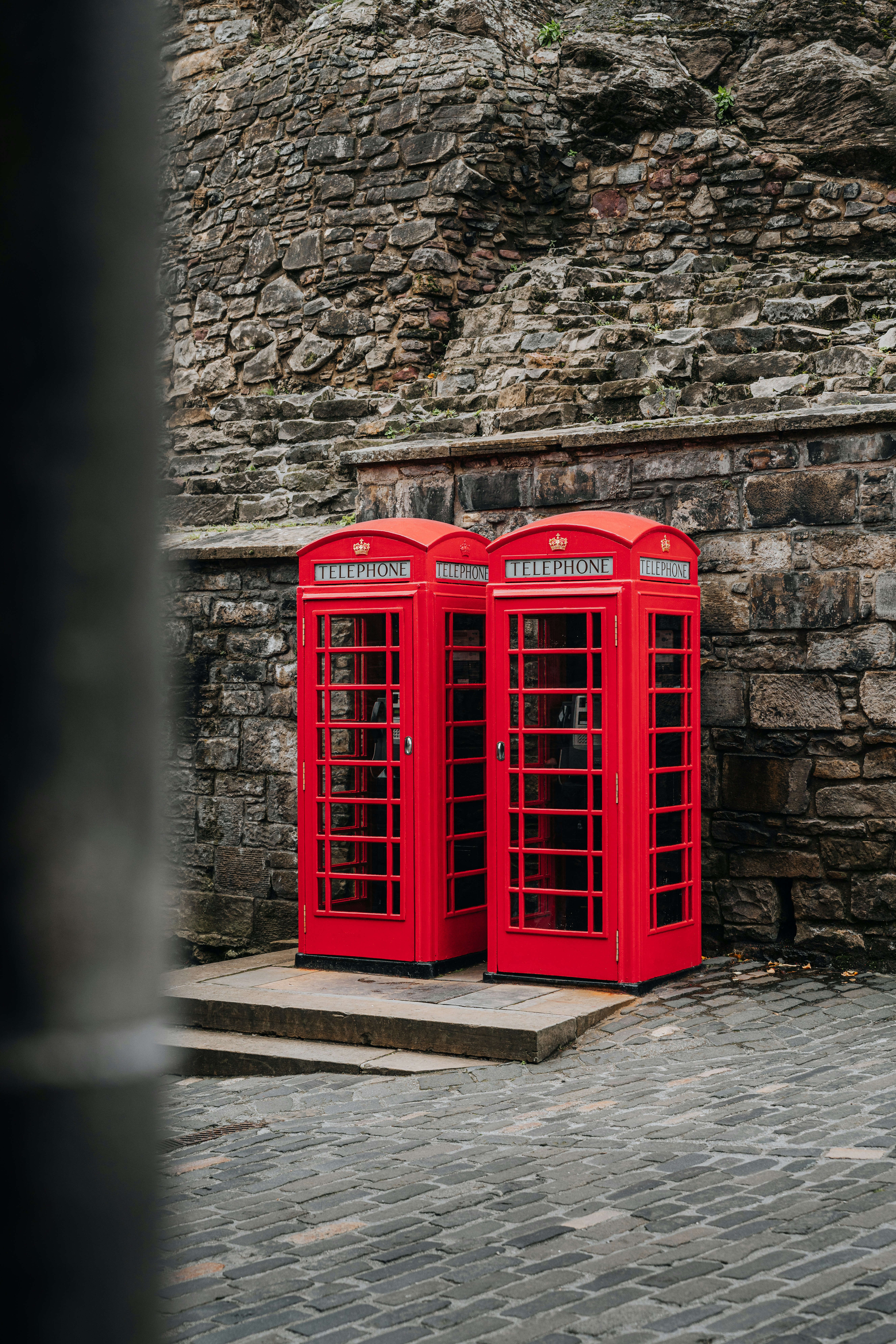 Crimson Duo: Red British Telephone Booths Guard the Weathered Stone Wall