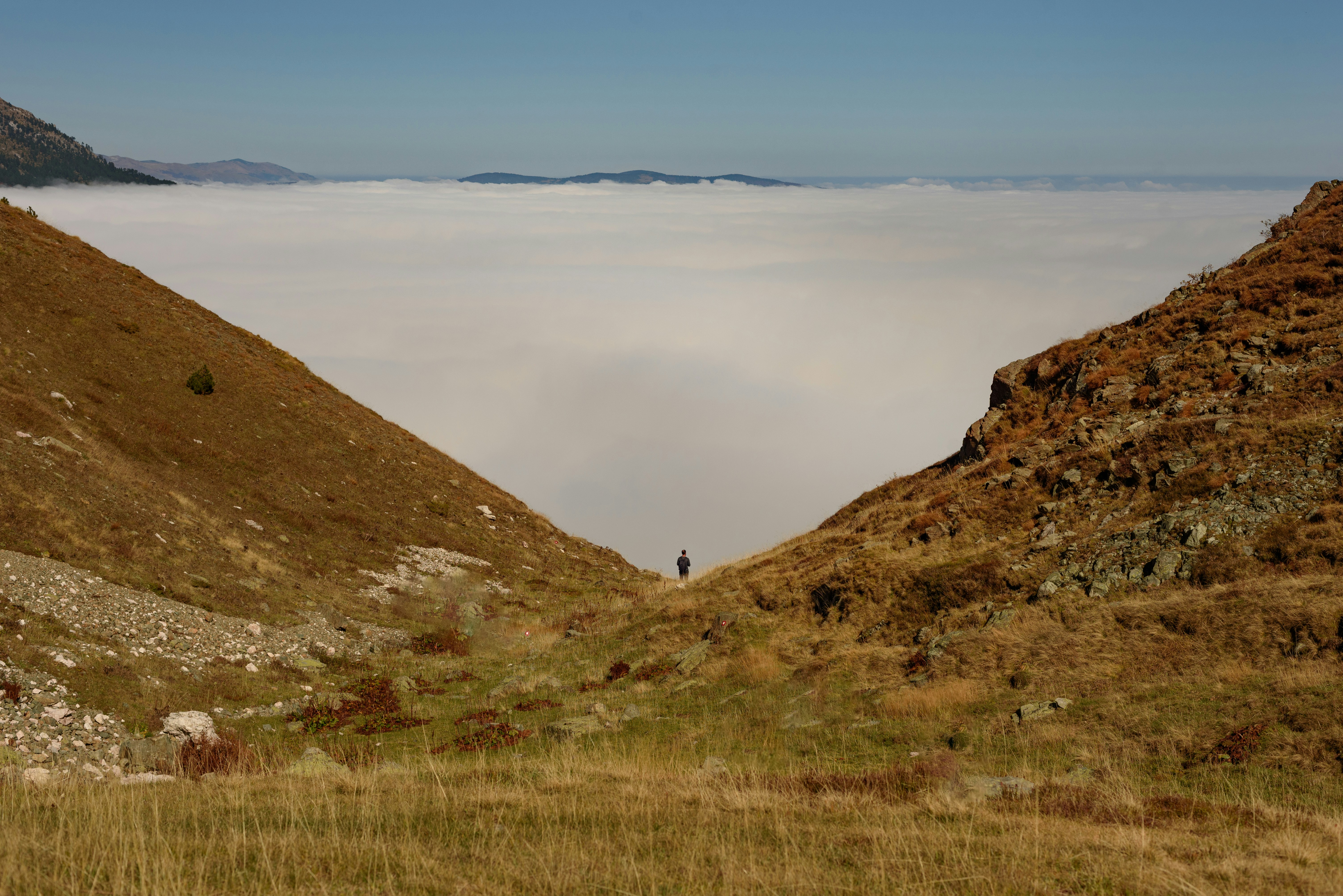 Hiker standing between two grassy mountains overlooking a vast cloud-filled valley.