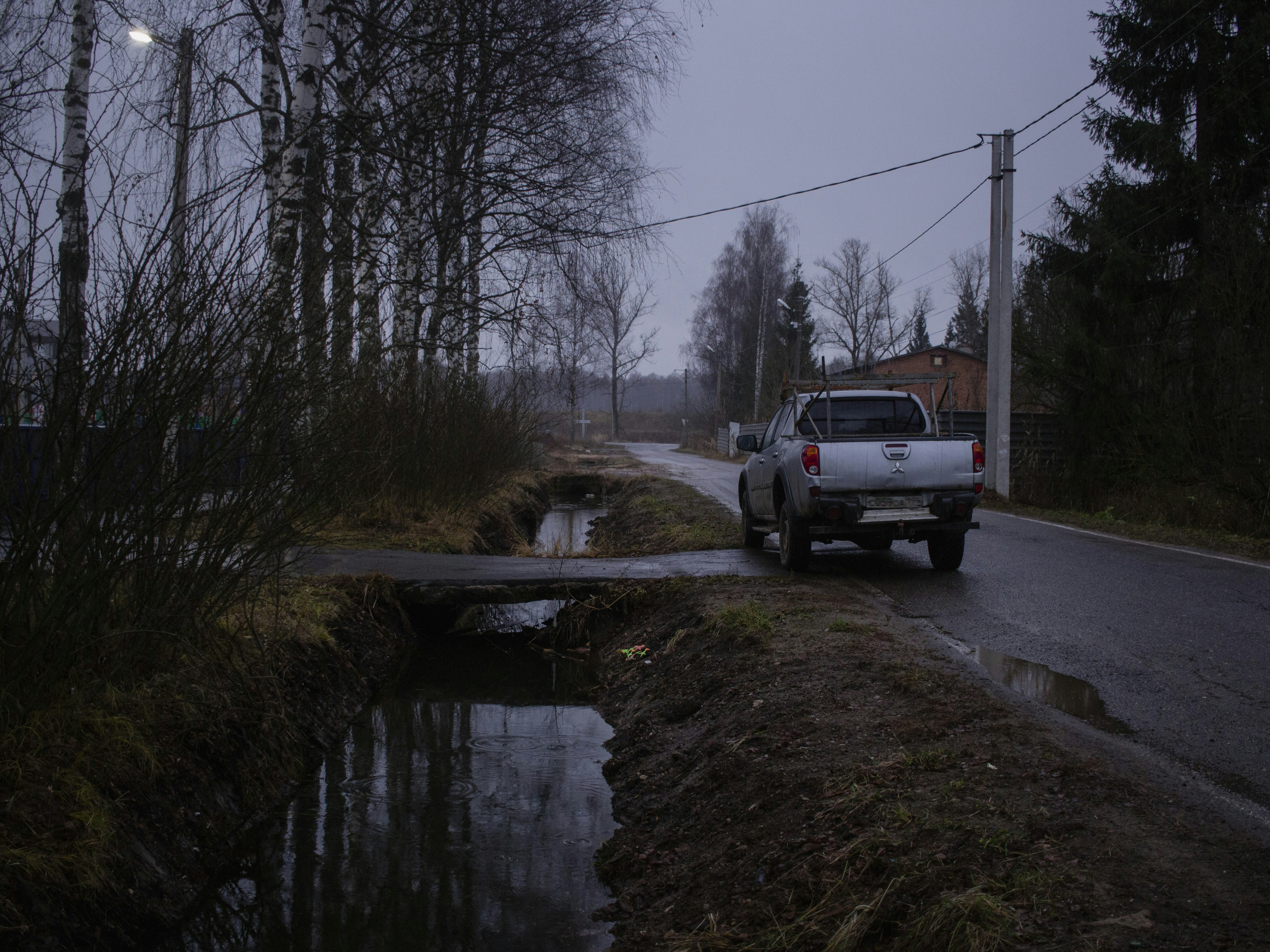 Silver Pickup on a Rain-Washed Rural Road Beside a Narrow Canal