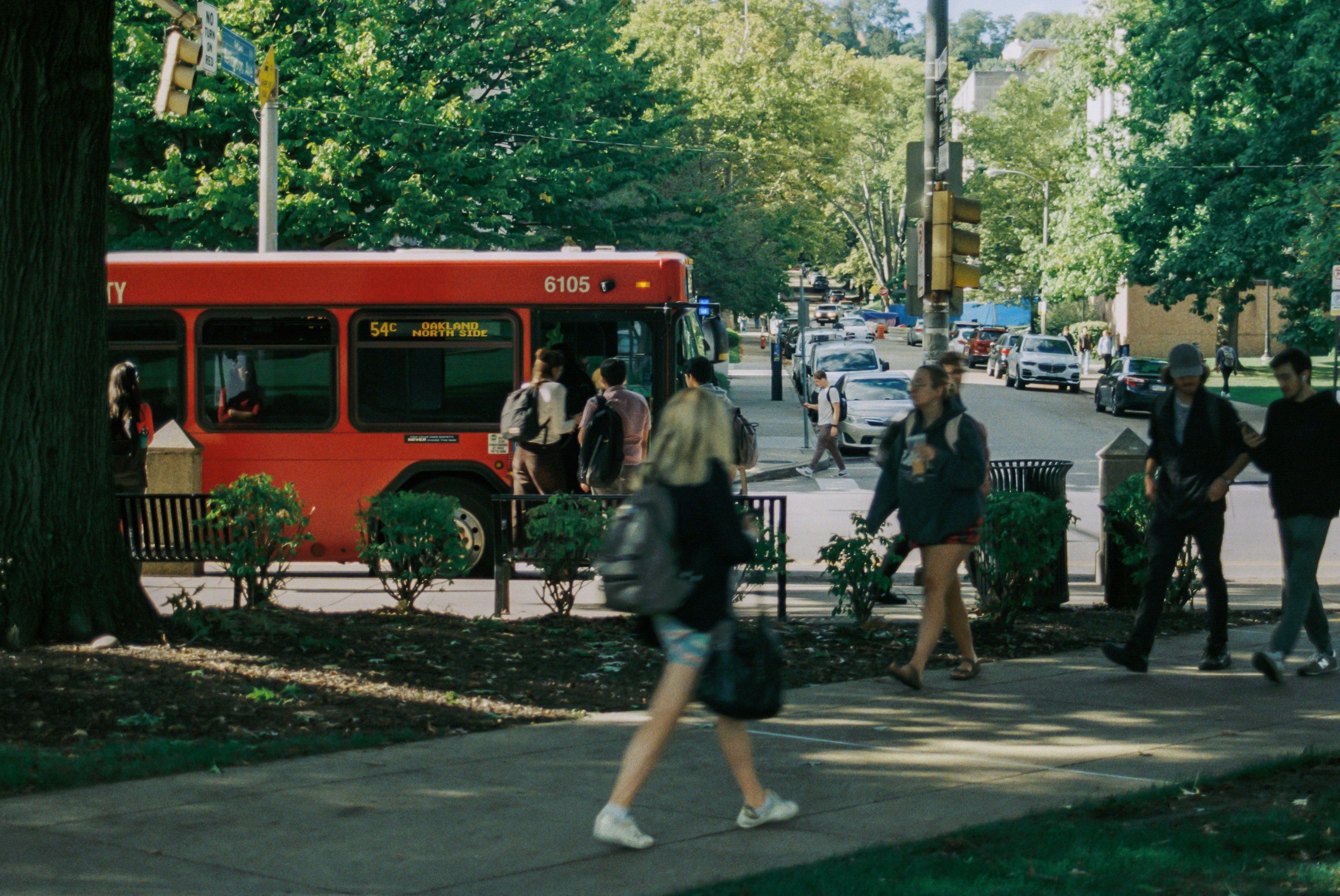 A group of people walking down a sidewalk next to a red bus photo ...