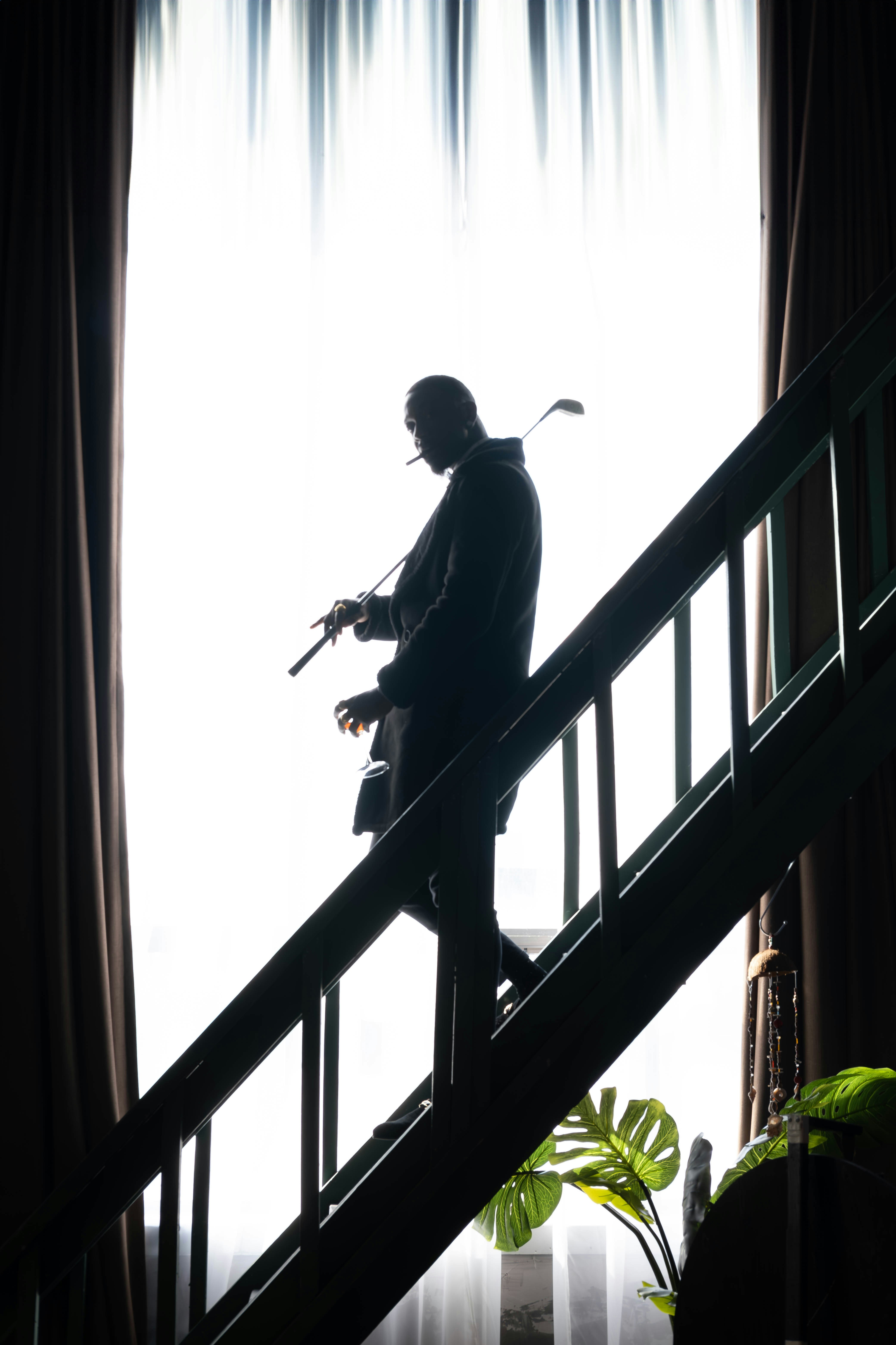 Staircase Silhouette: Hooded Figure with a Blade in Backlit Silence