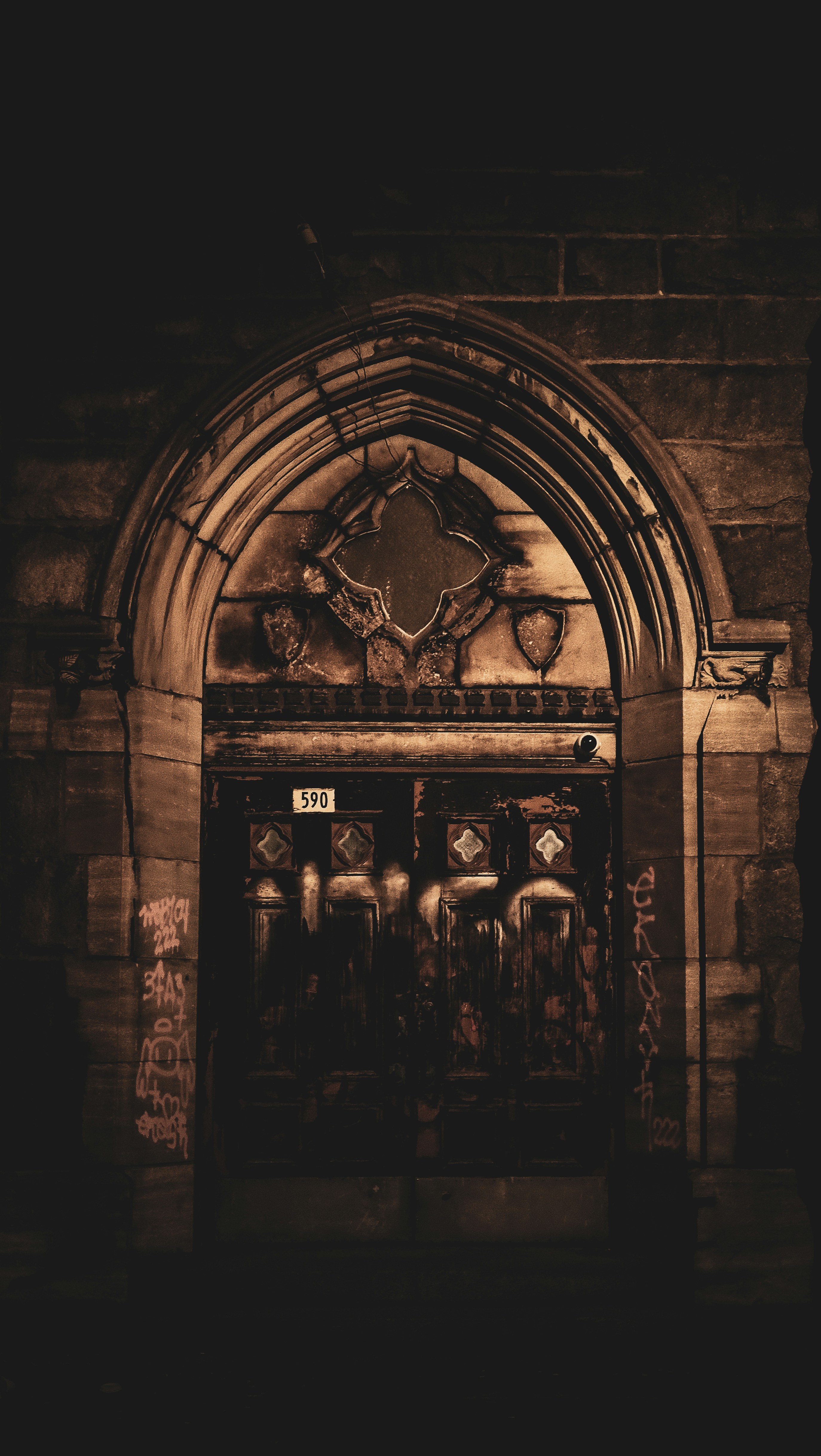 Photograph of a graffiti-splashed Gothic doorway framed by a stone arch, lit in sepia tones.