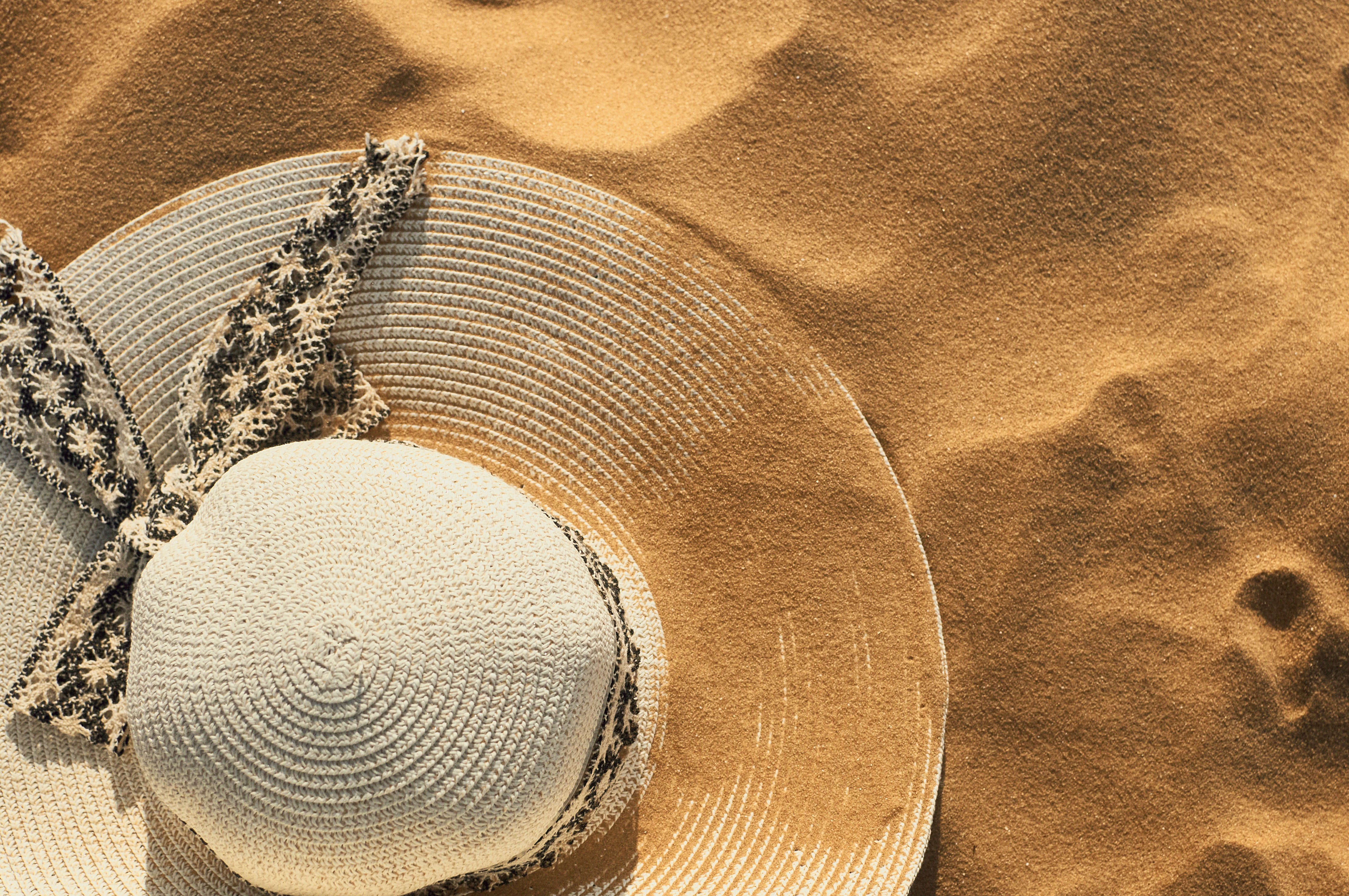 Stylish sunhat with intricate ribbon detail nestled on golden sand, embodying summer's warmth and tranquility.