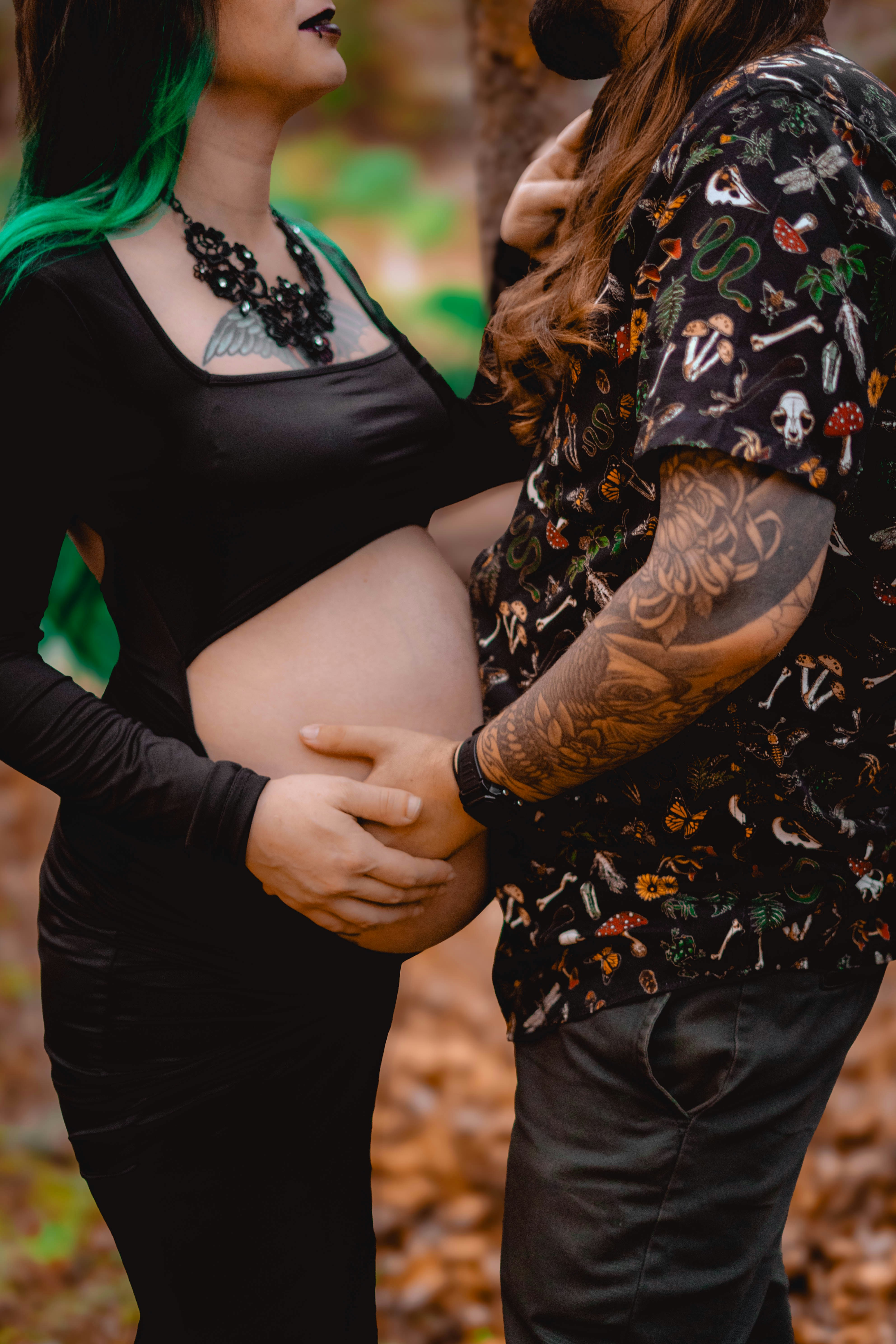 Expectant couple embracing in a forest, surrounded by vibrant autumn leaves.