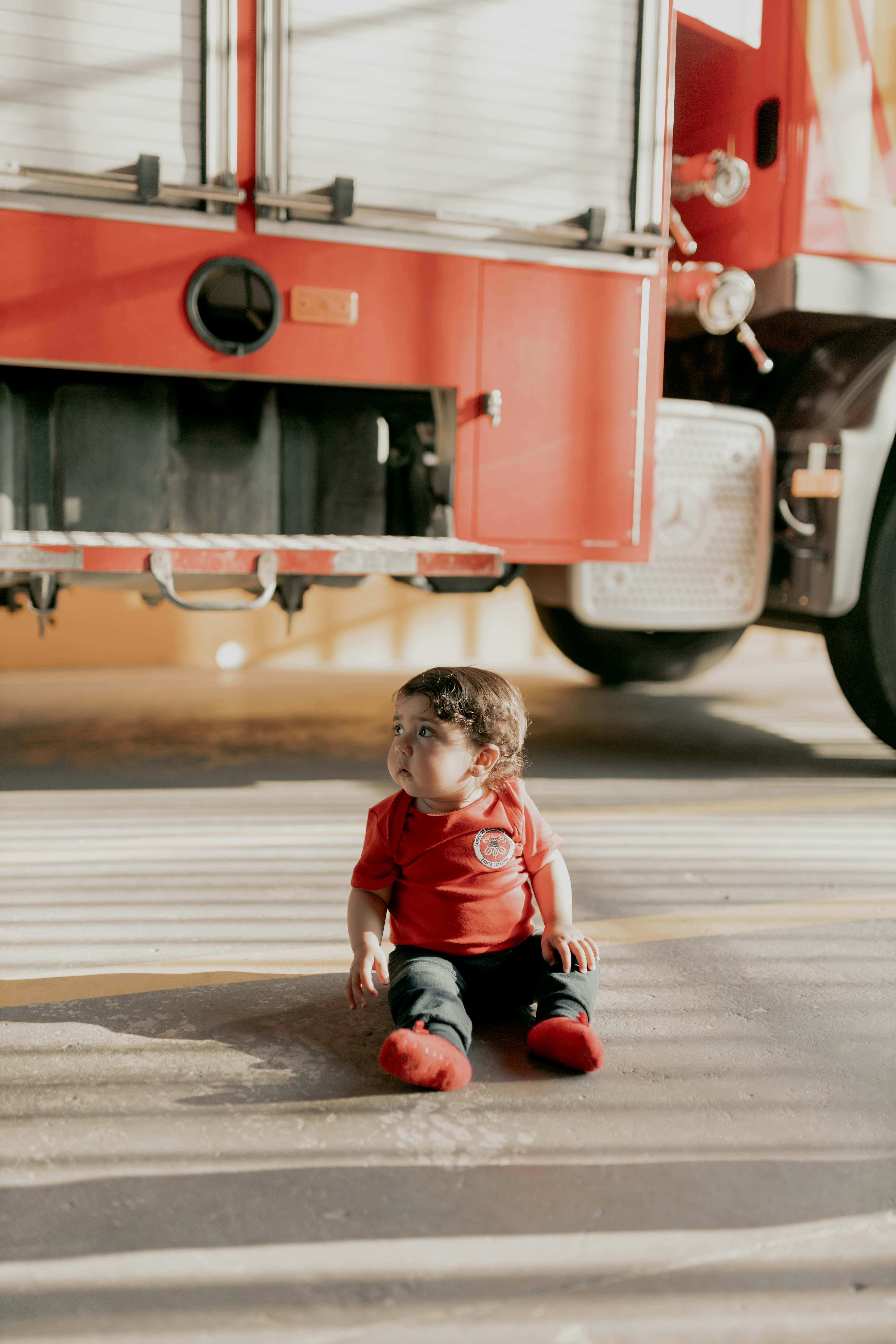 Firetruck Underfoot: A Curious Toddler Pauses in Red