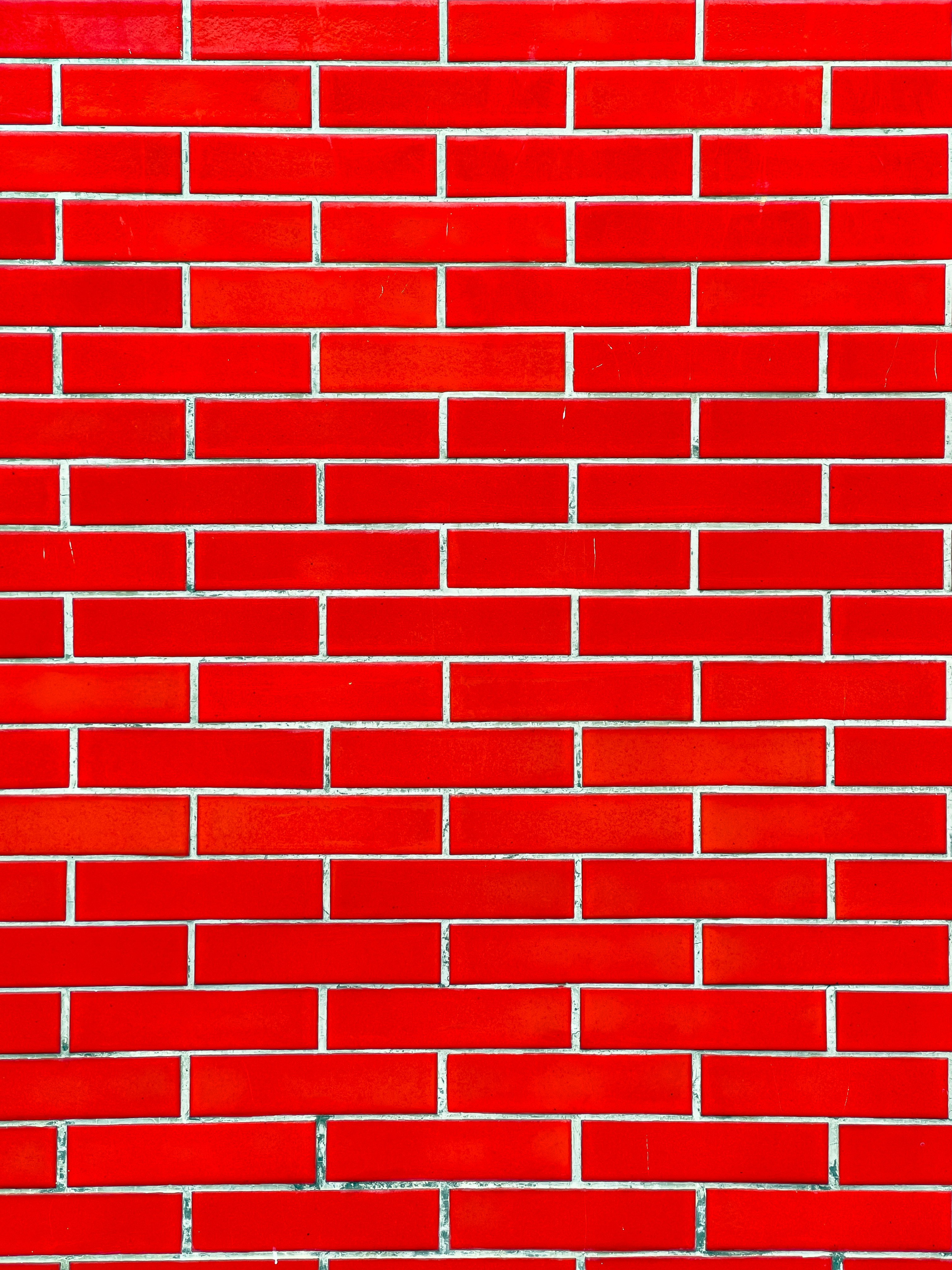 --- A red brick wall featuring evenly arranged rectangular tiles, creating a vibrant and cleanly patterned surface. The bright red color of the bricks stands out, adding visual impact to the simple architectural design.