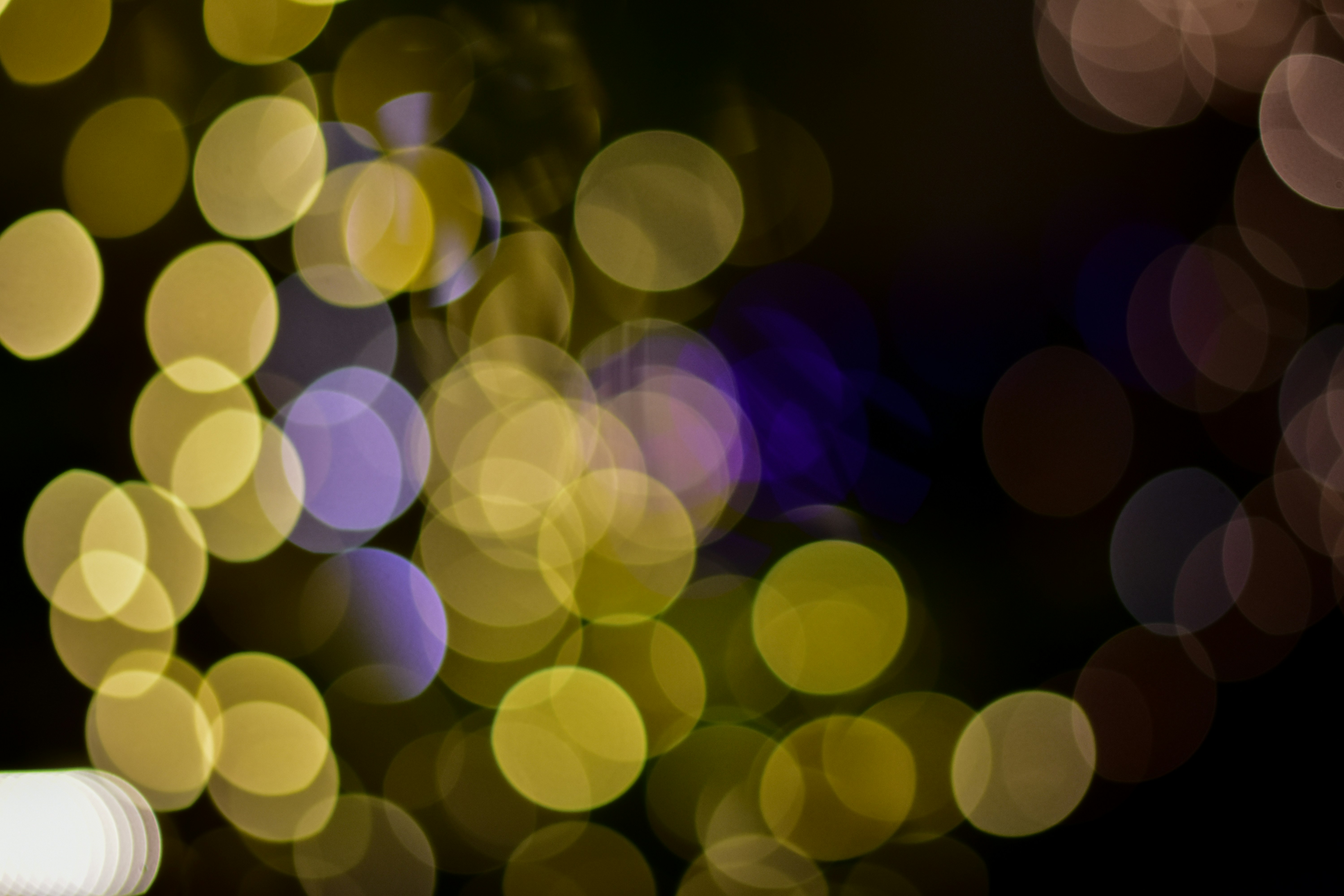 A vibrant display of bokeh lights blending yellow, purple, and soft hues against a dark backdrop, creating an abstract visual experience.