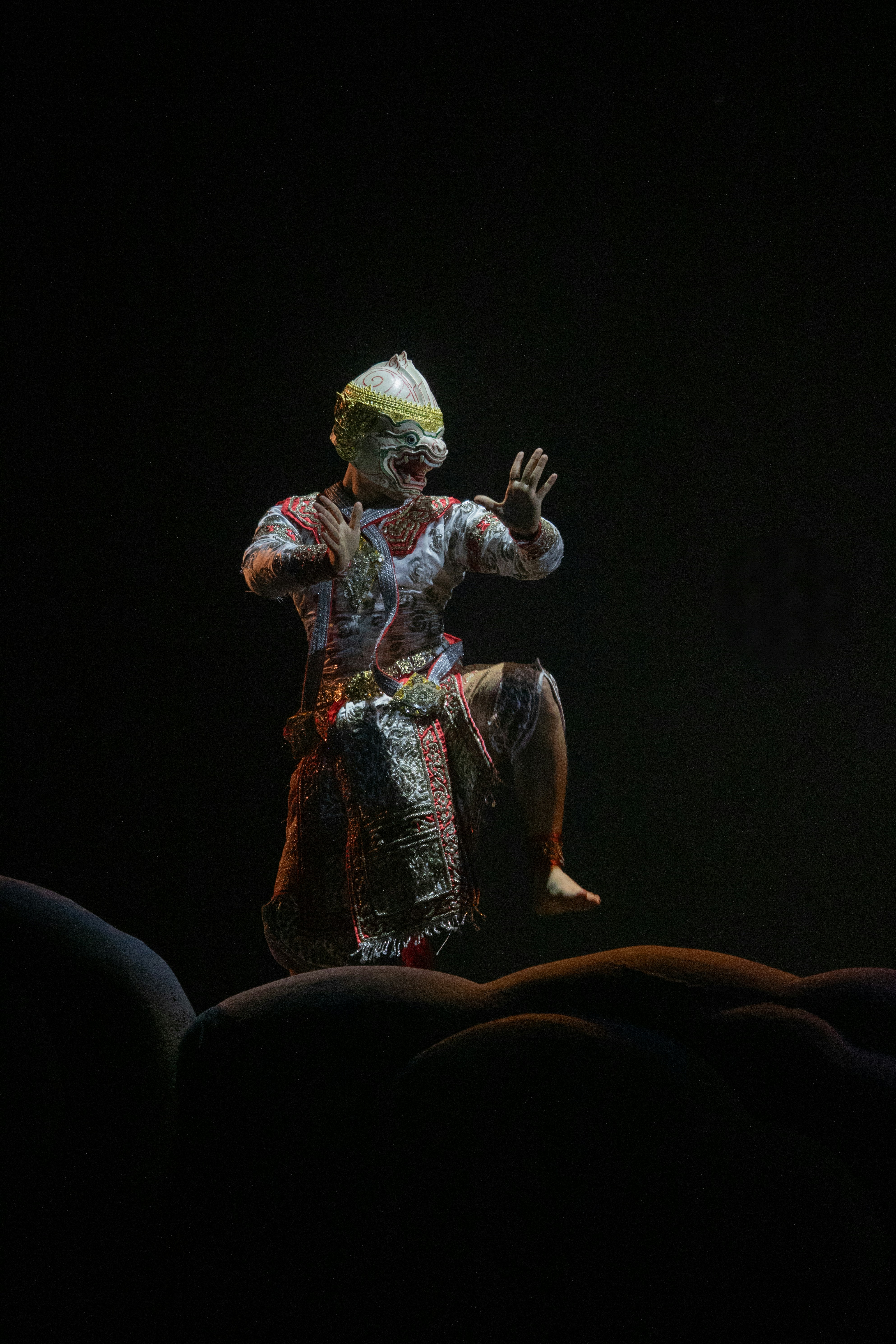 Masked performer suspended in a velvet-dark stage