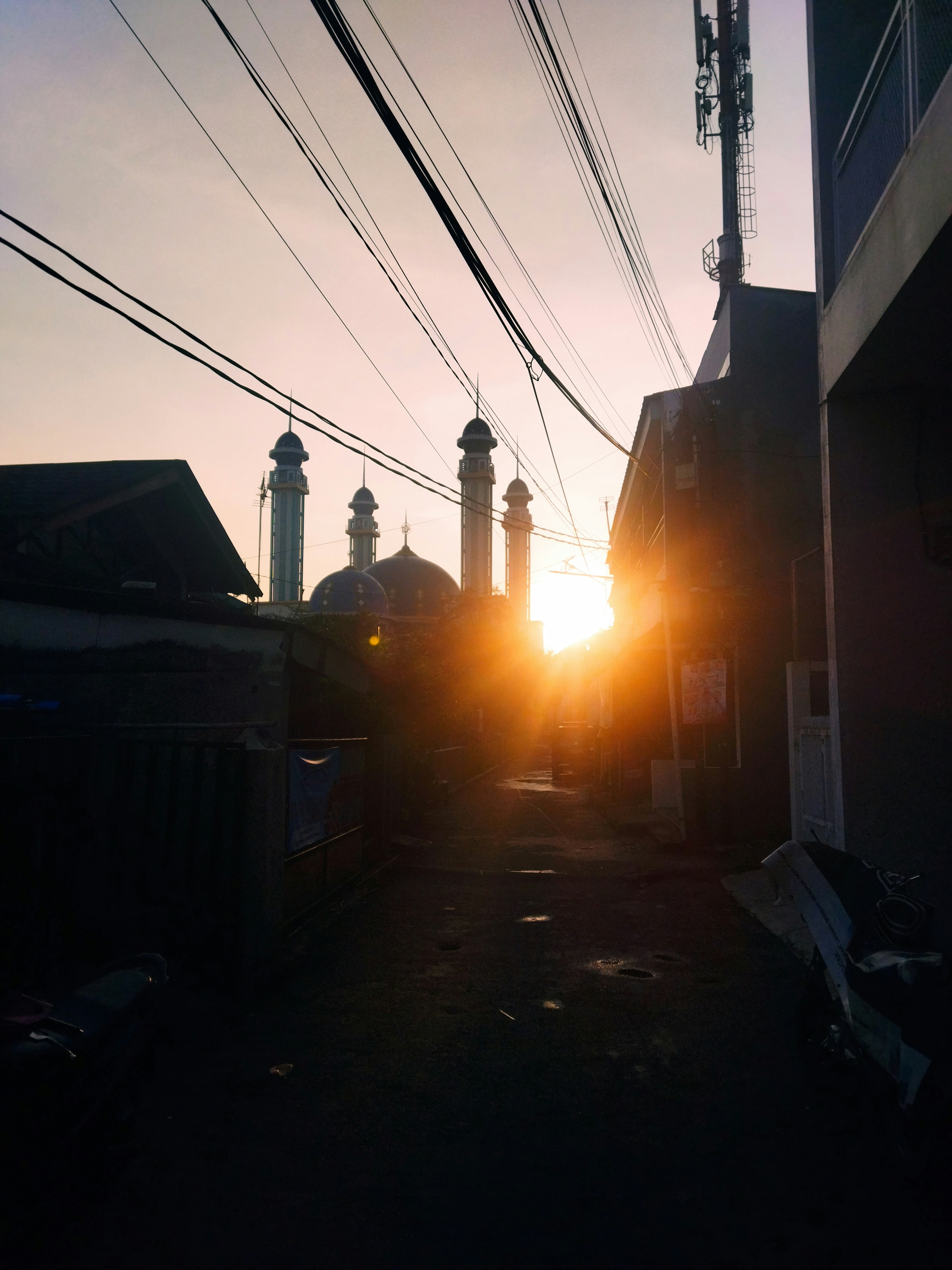 Sunlit alley toward a mosque skyline at sunset, with crisscrossing power lines overhead.