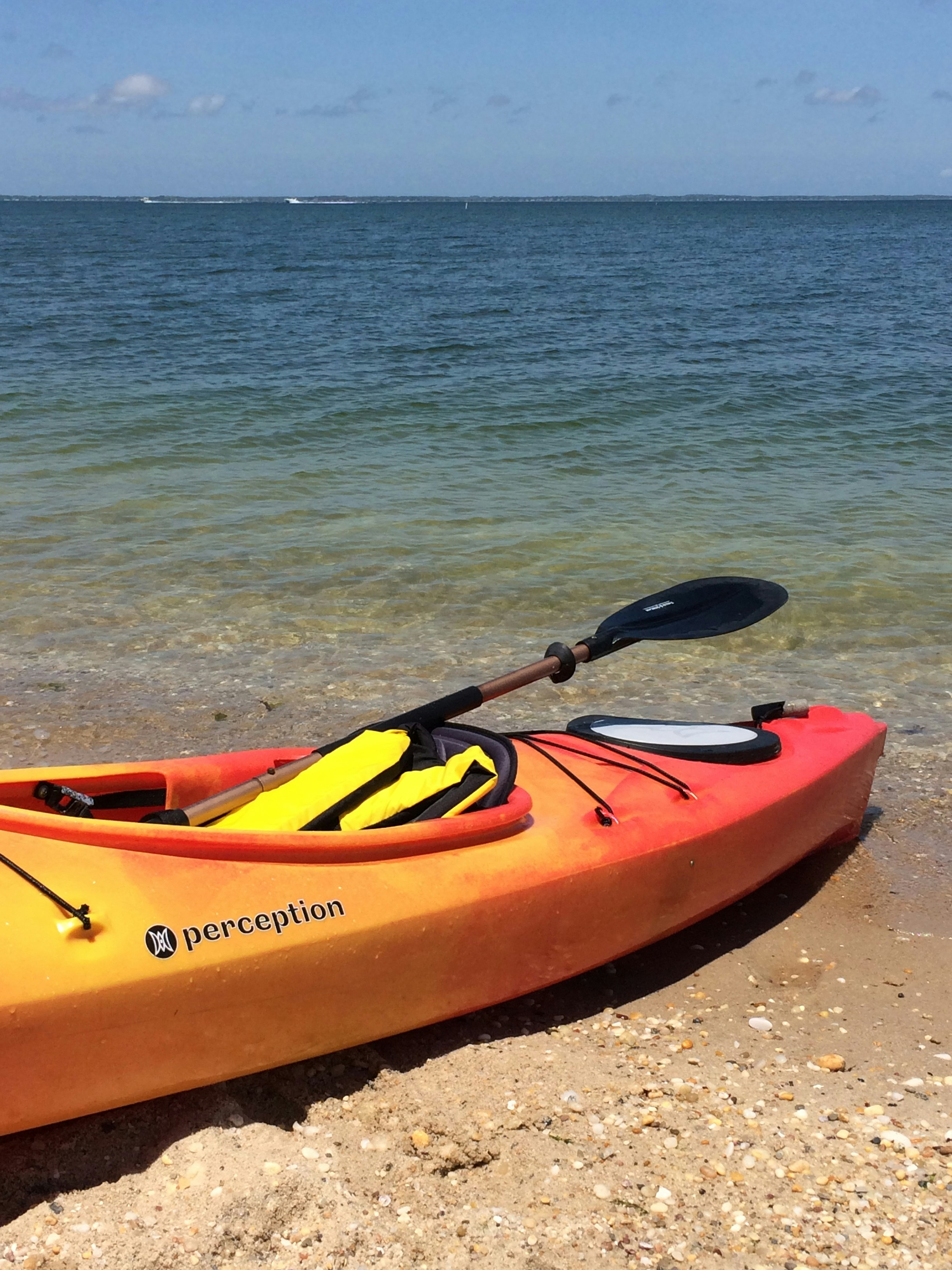 Sunlit Orange Kayak on a Pebble Beach as Quiet Seas Meet the Shore