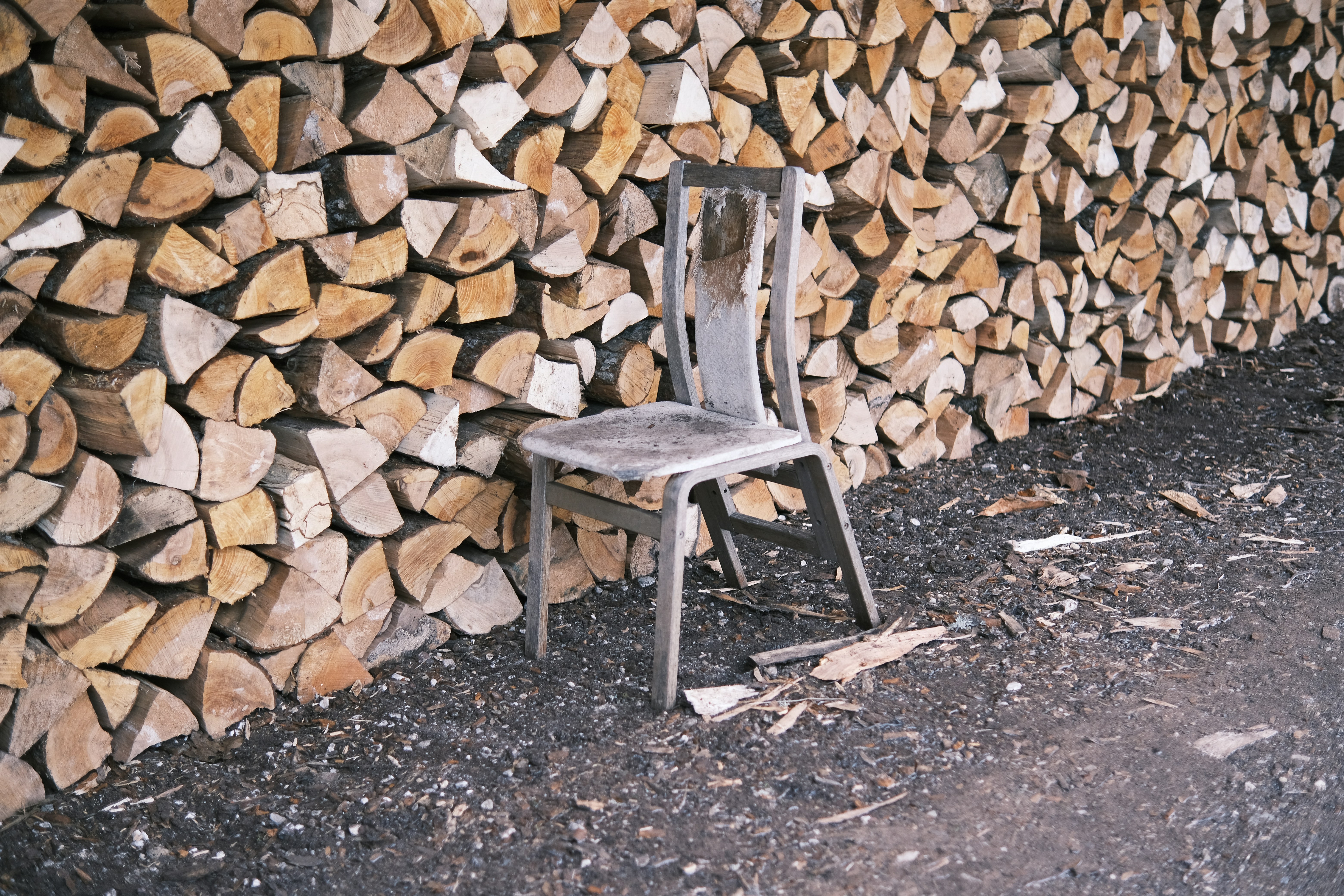 Weathered Chair Standing Guard Over a Stacked Wood Wall