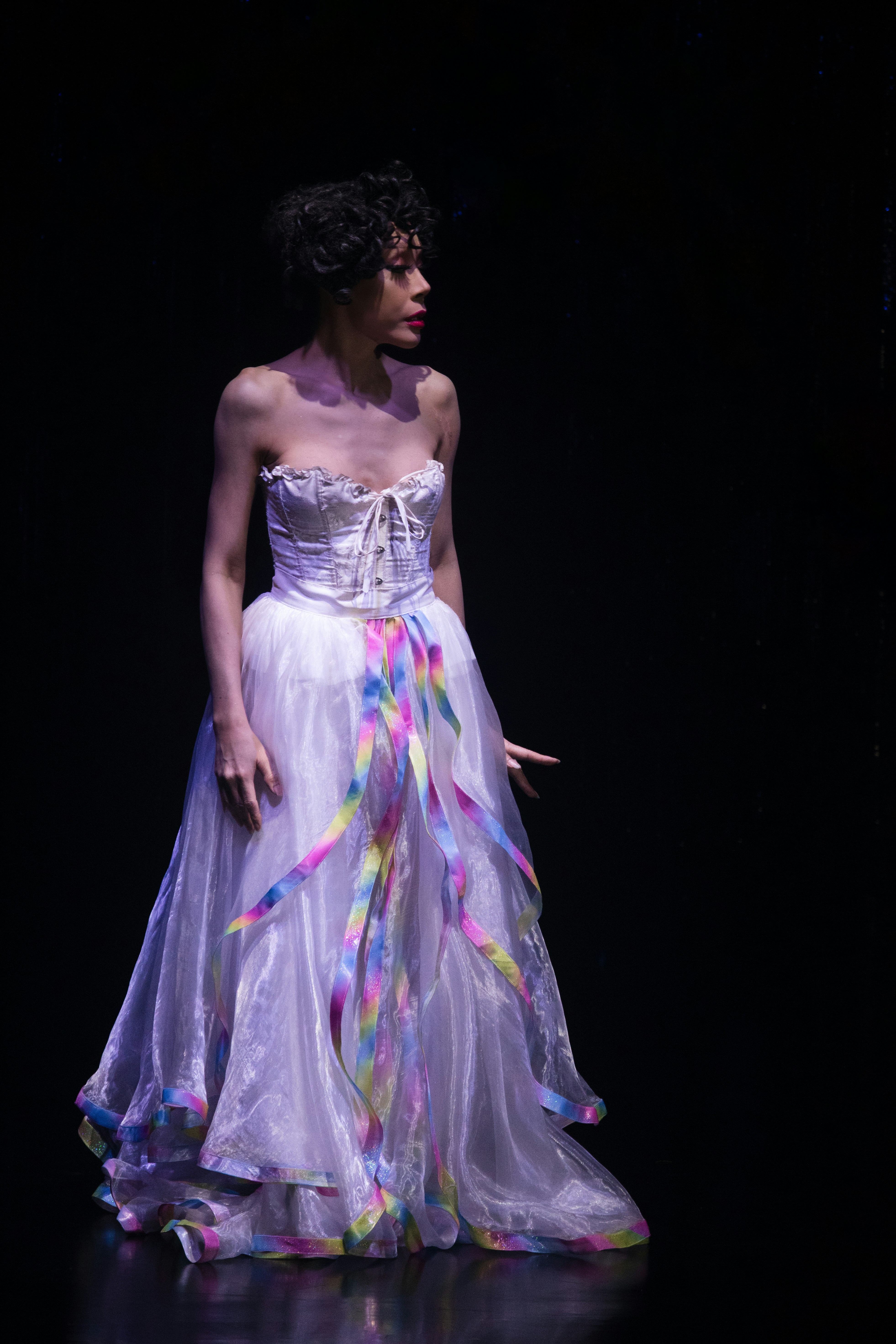 Spotlight Sonata: A Dancer in a Rainbow-Wed Dress Emerges from Velvet Darkness