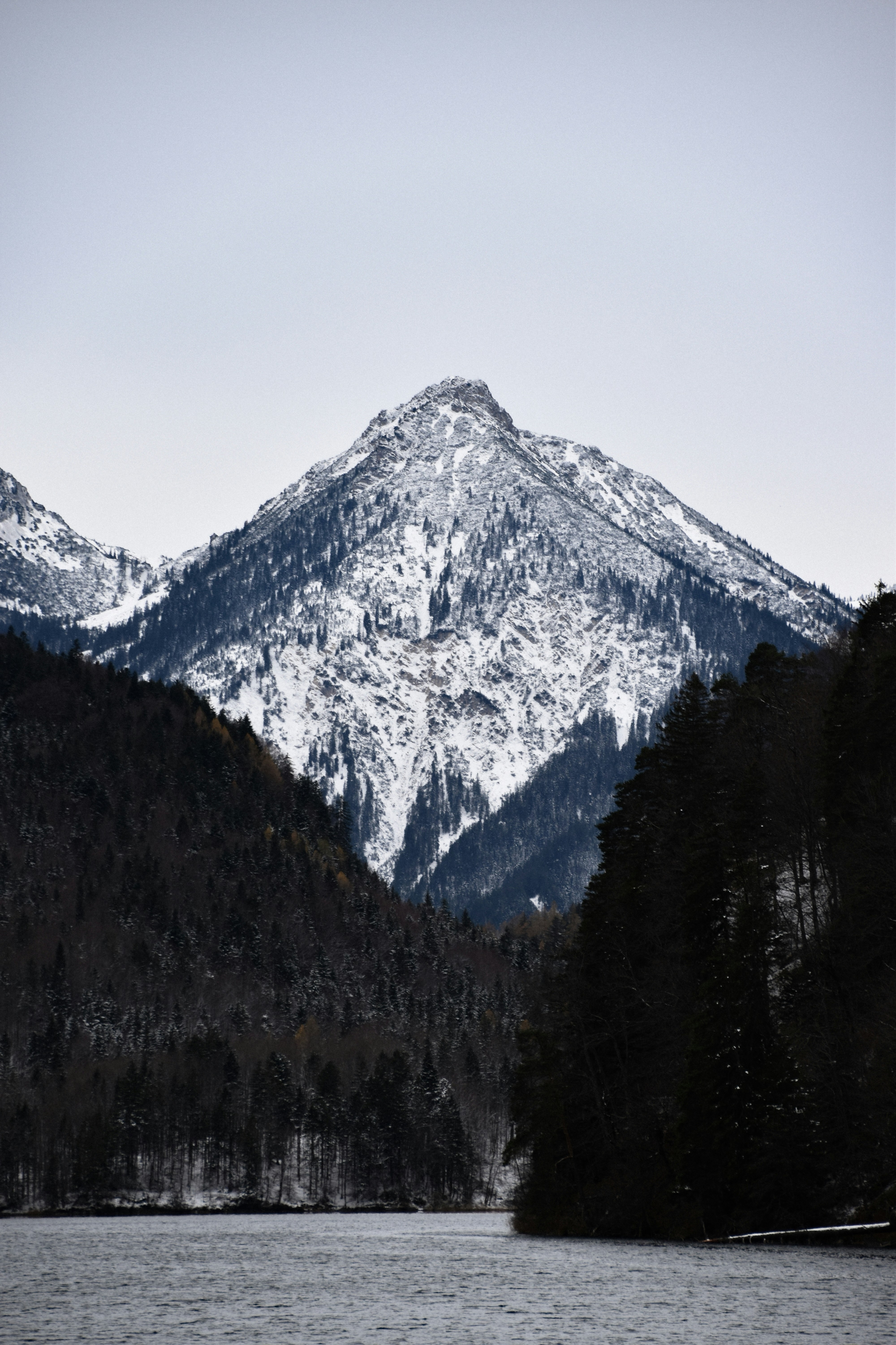 Snow-covered mountain towering over a tranquil lake surrounded by evergreen trees.