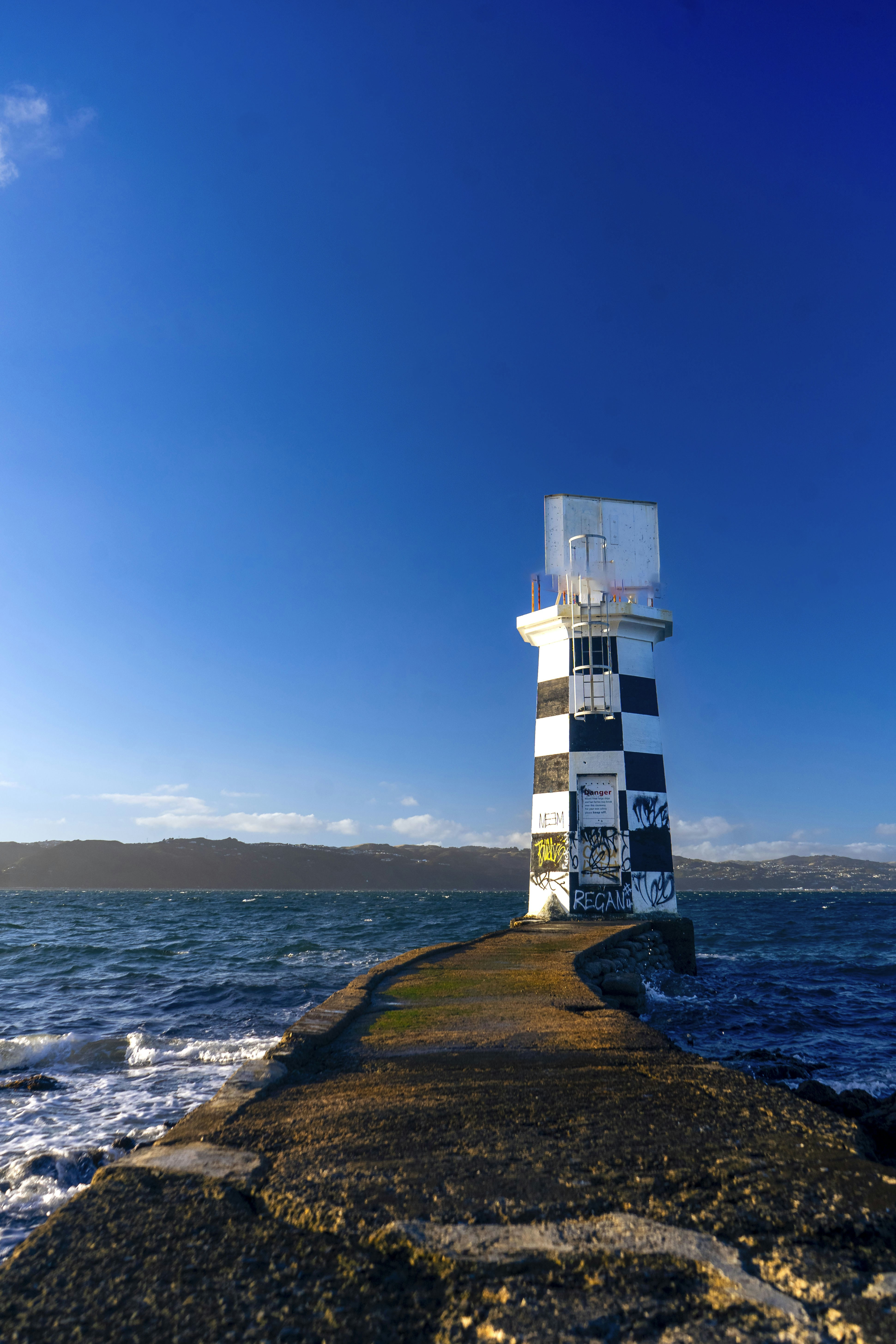 Checkered Lighthouse at the End of a Sunlit Breakwater