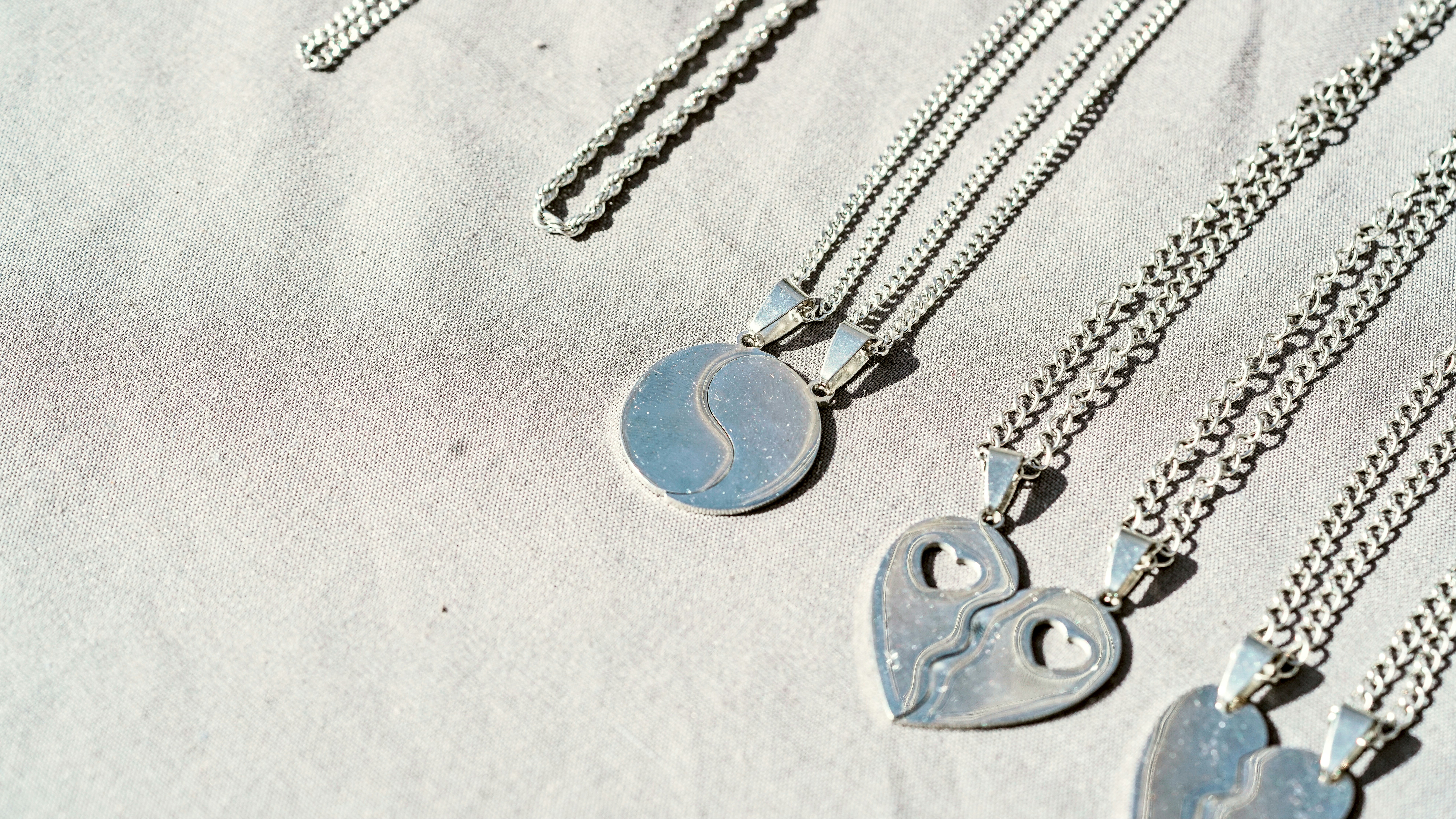 Silver pendants with intricate designs displayed on a fabric surface under natural light.