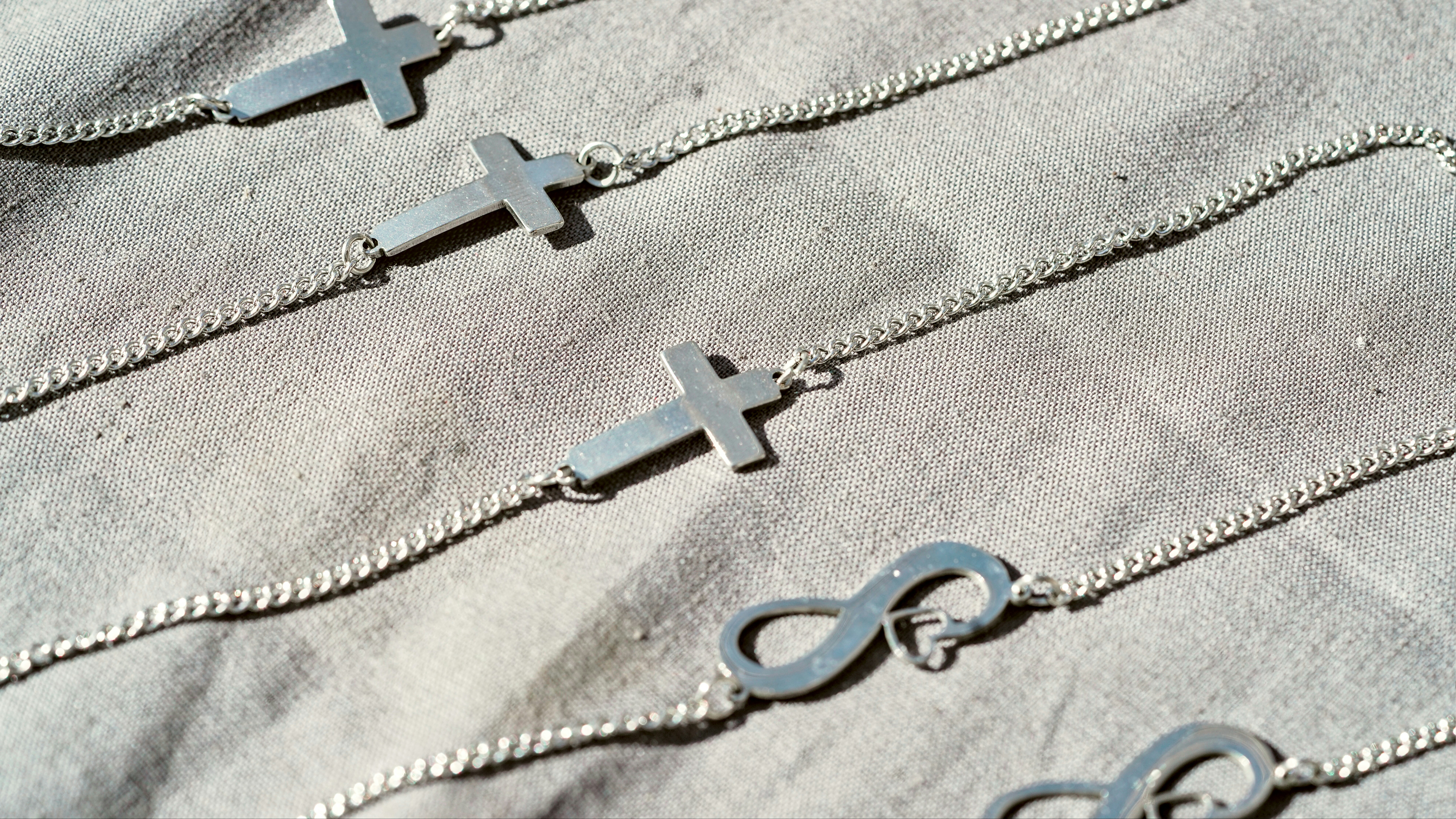 Infinity and Crosses: Close-Up of Silver Jewelry on Textured Gray Fabric