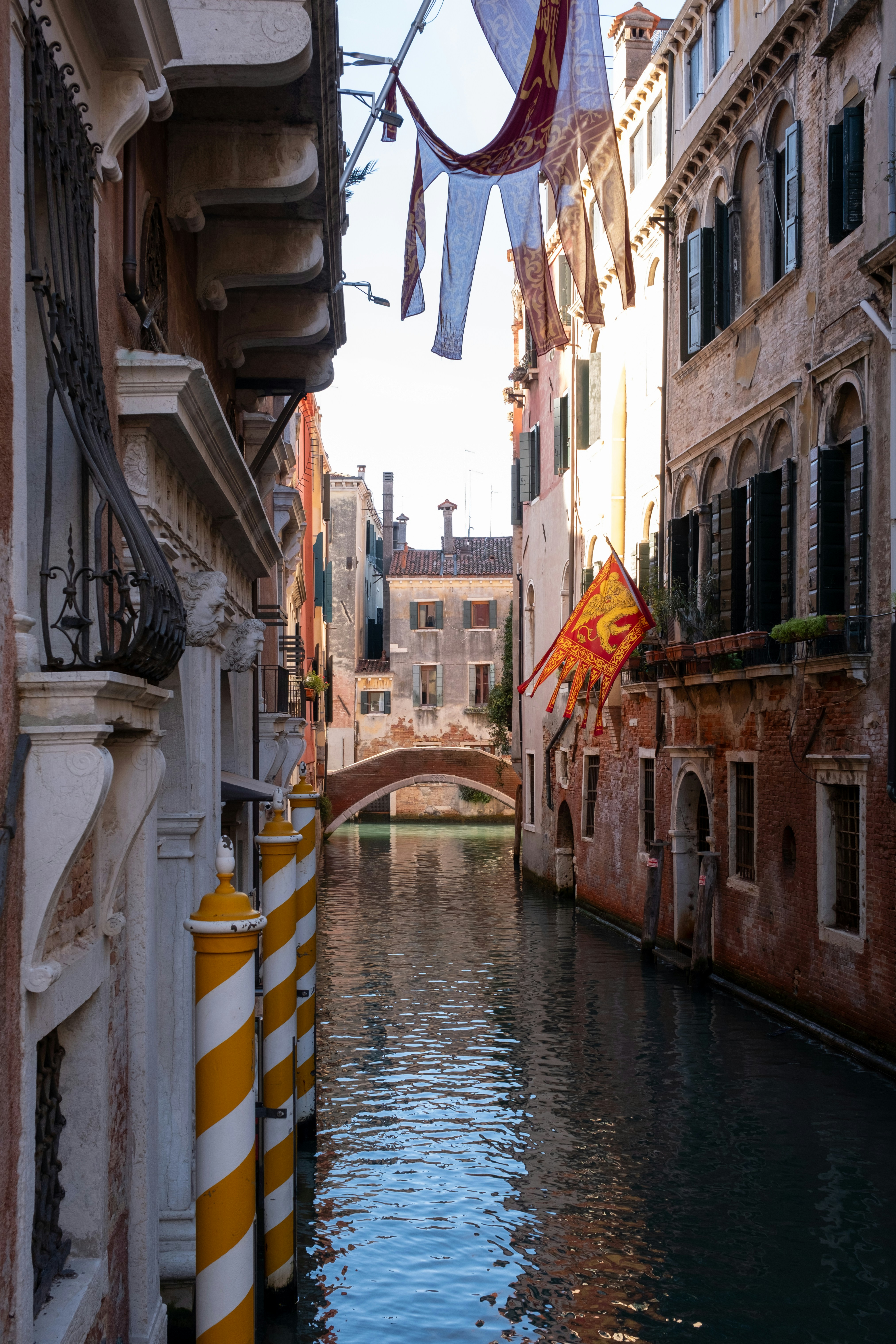 Venice Canal in Warm Light: Flags, Water, and a Distant Bridge