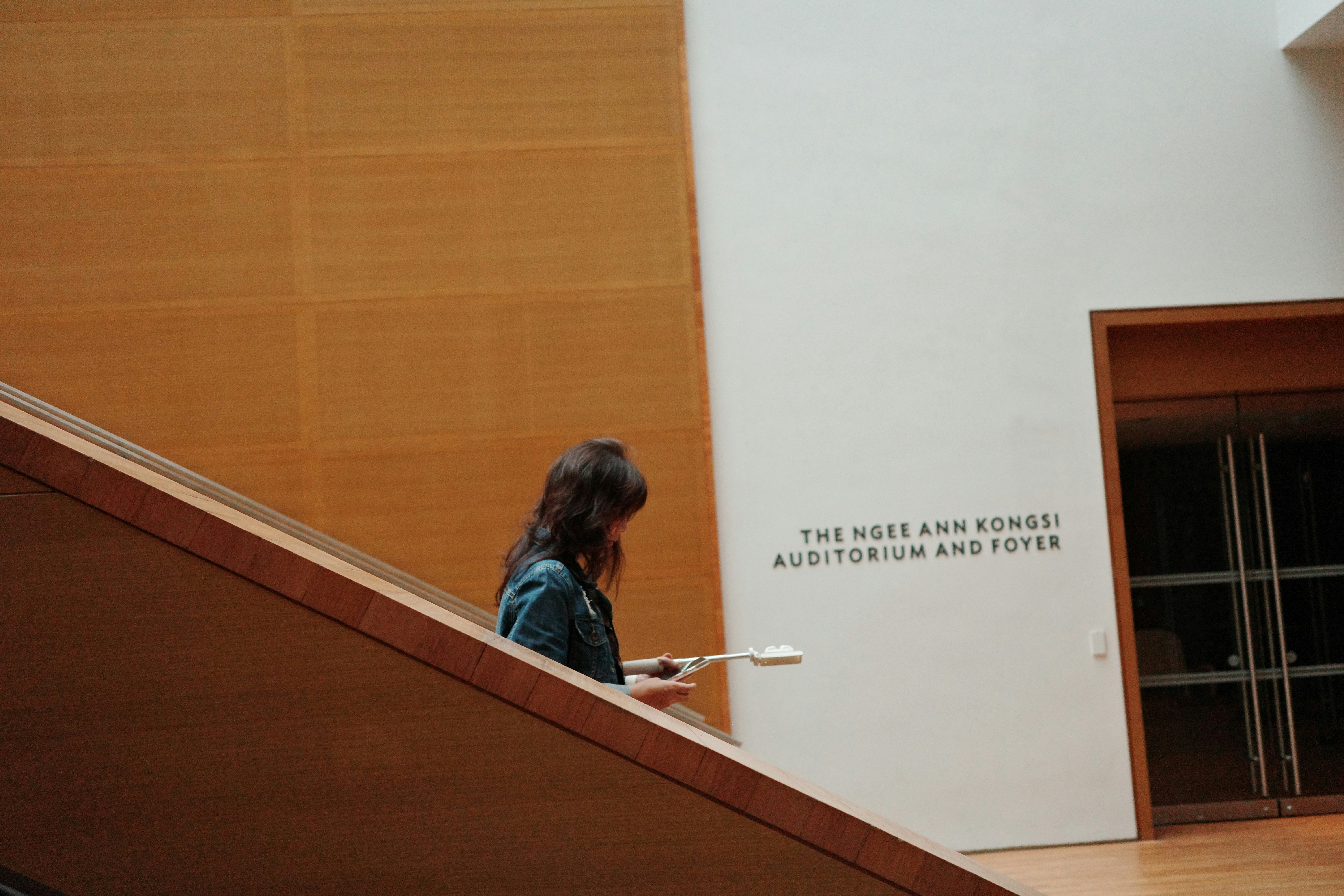 Guitar in Hand on a Slanted Wooden Ramp in a Minimalist Auditorium Foyer