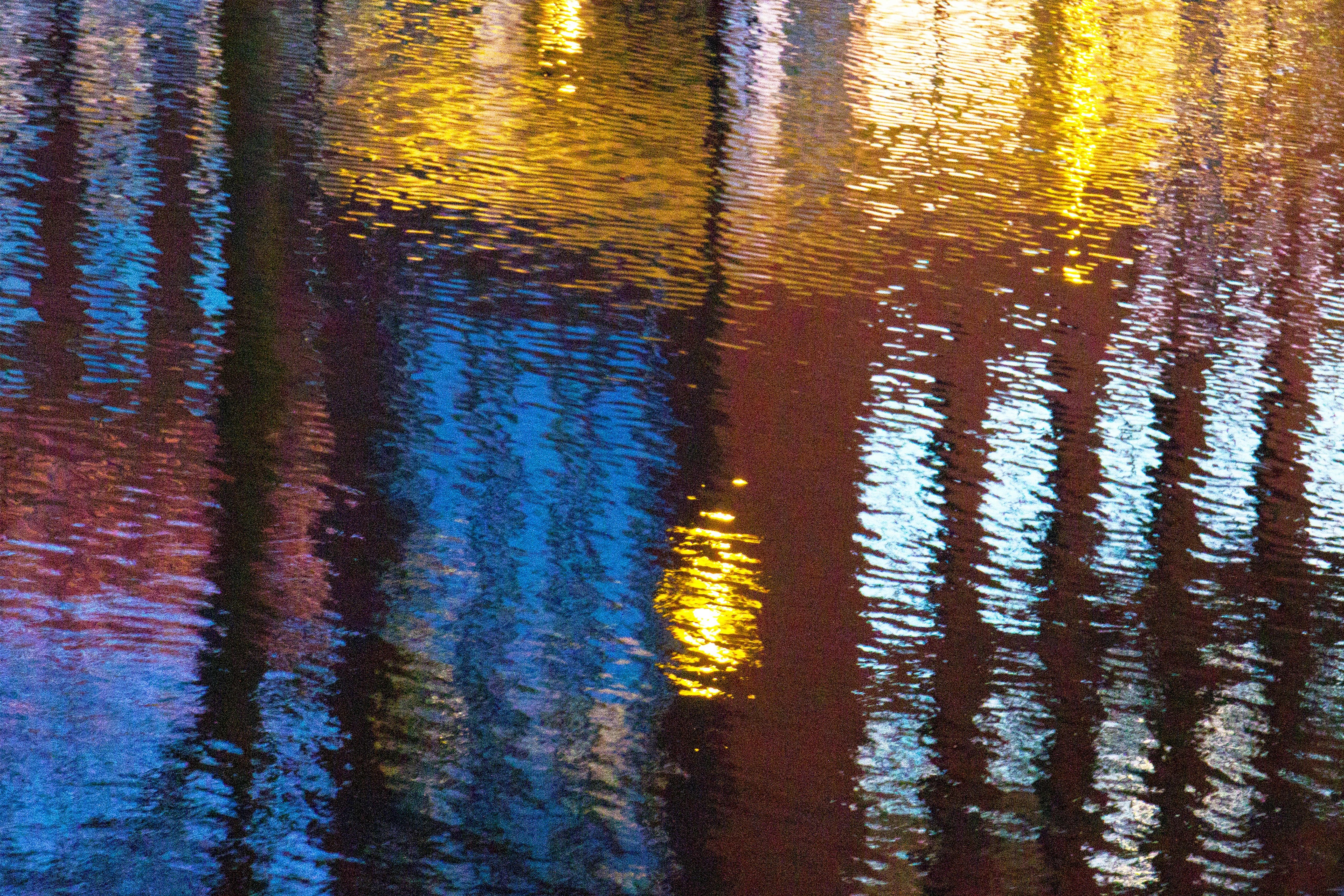 Vivid reflections of colorful city lights ripple across a water surface at night.