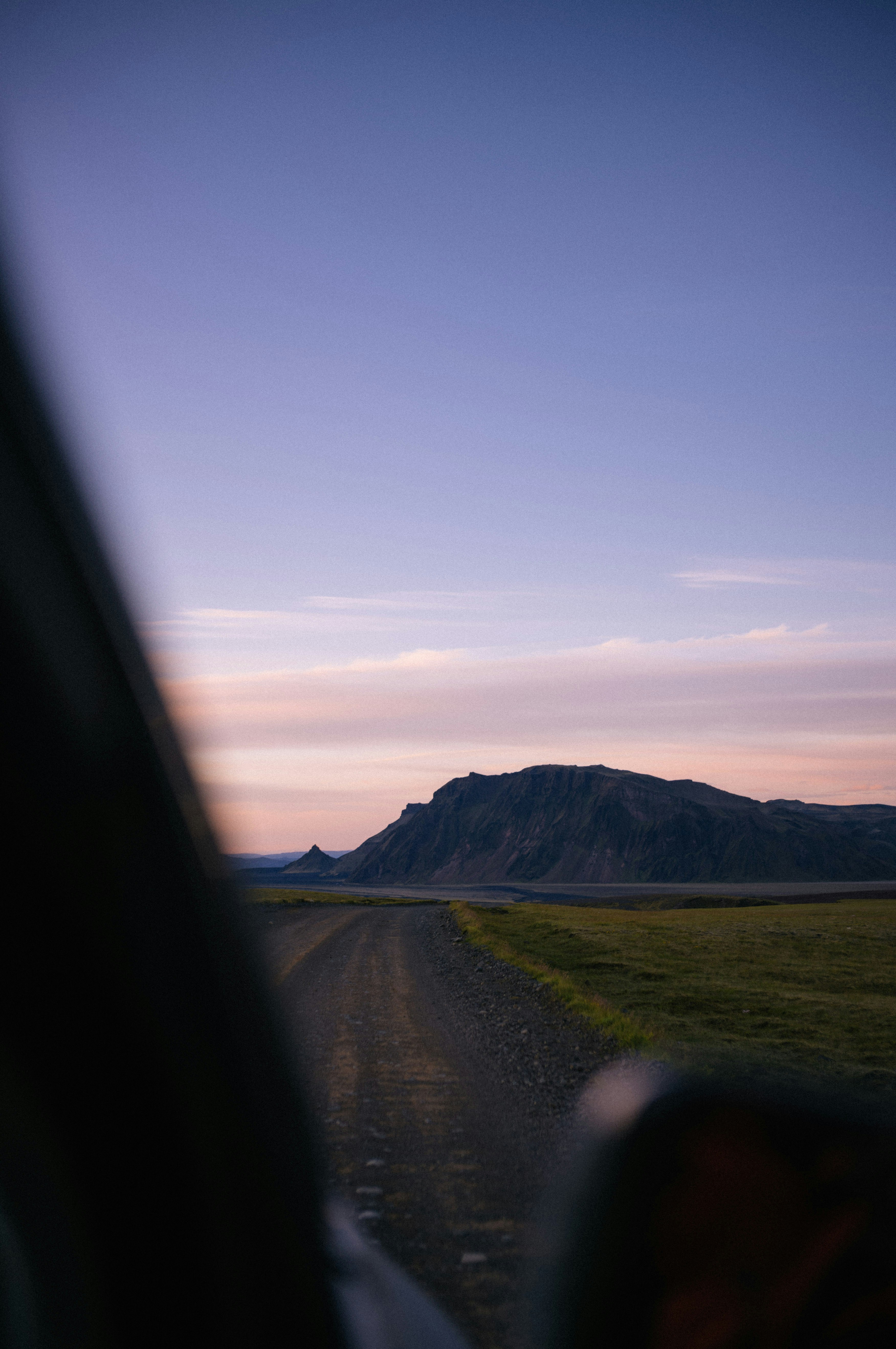 Rugged mountain range under a serene twilight sky with a road leading towards distant silhouettes, framed by purple and pink hues.