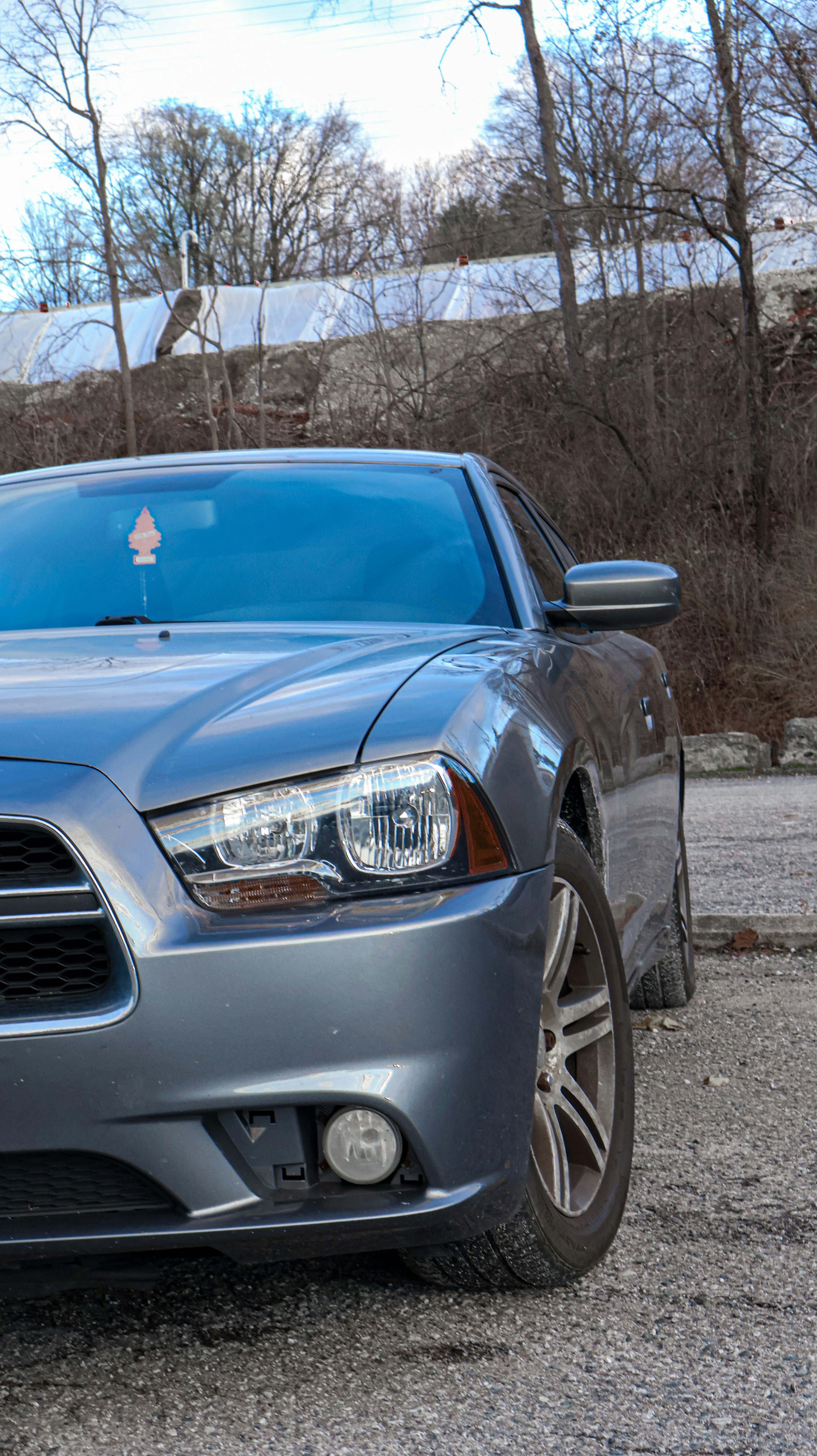 Front-Quarter Calm: Metallic Blue Sedan Resting at the Edge of a Gravel Lot