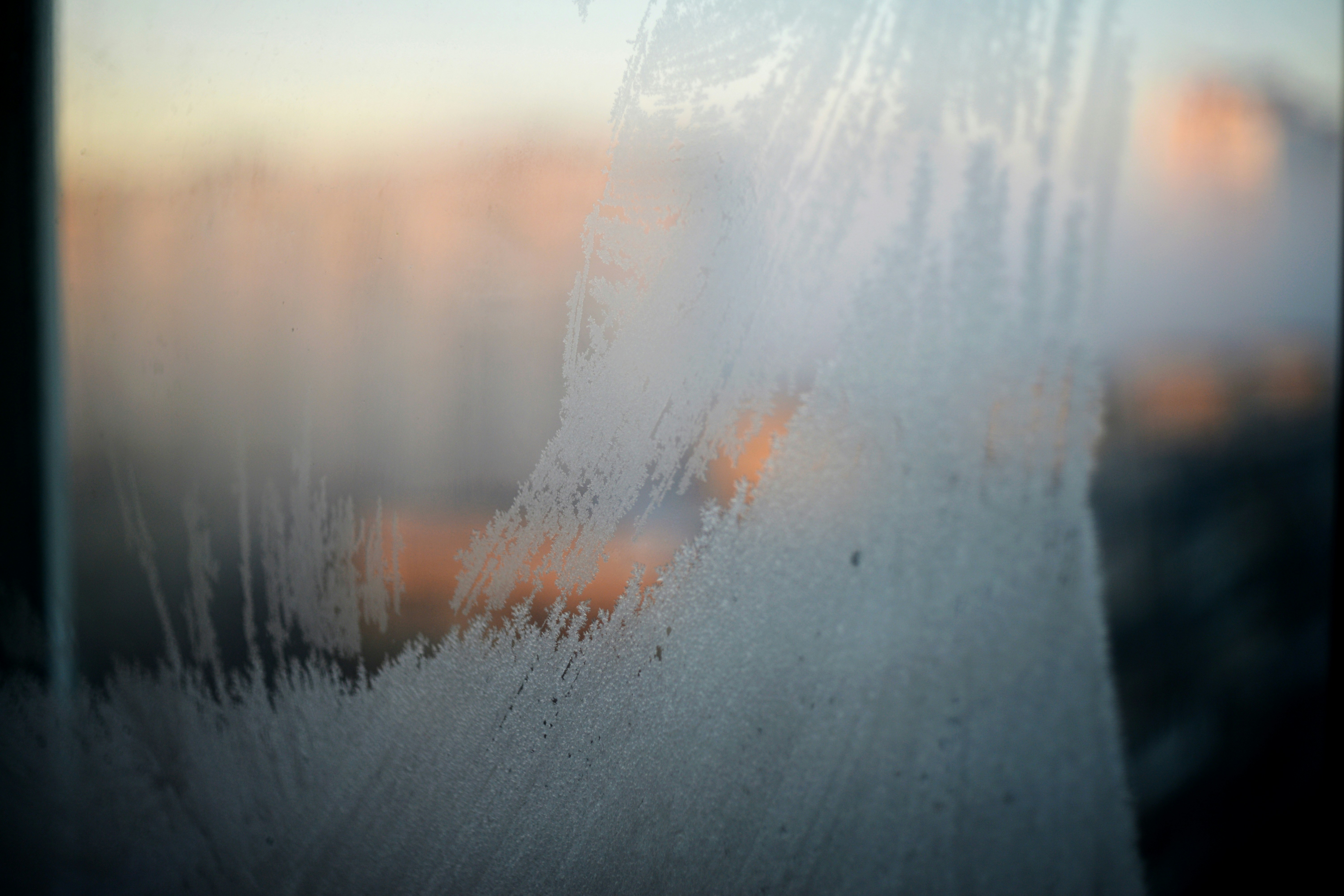 Frost patterns etched on a window, with soft morning light illuminating the icy details. The scene conveys a serene winter atmosphere.