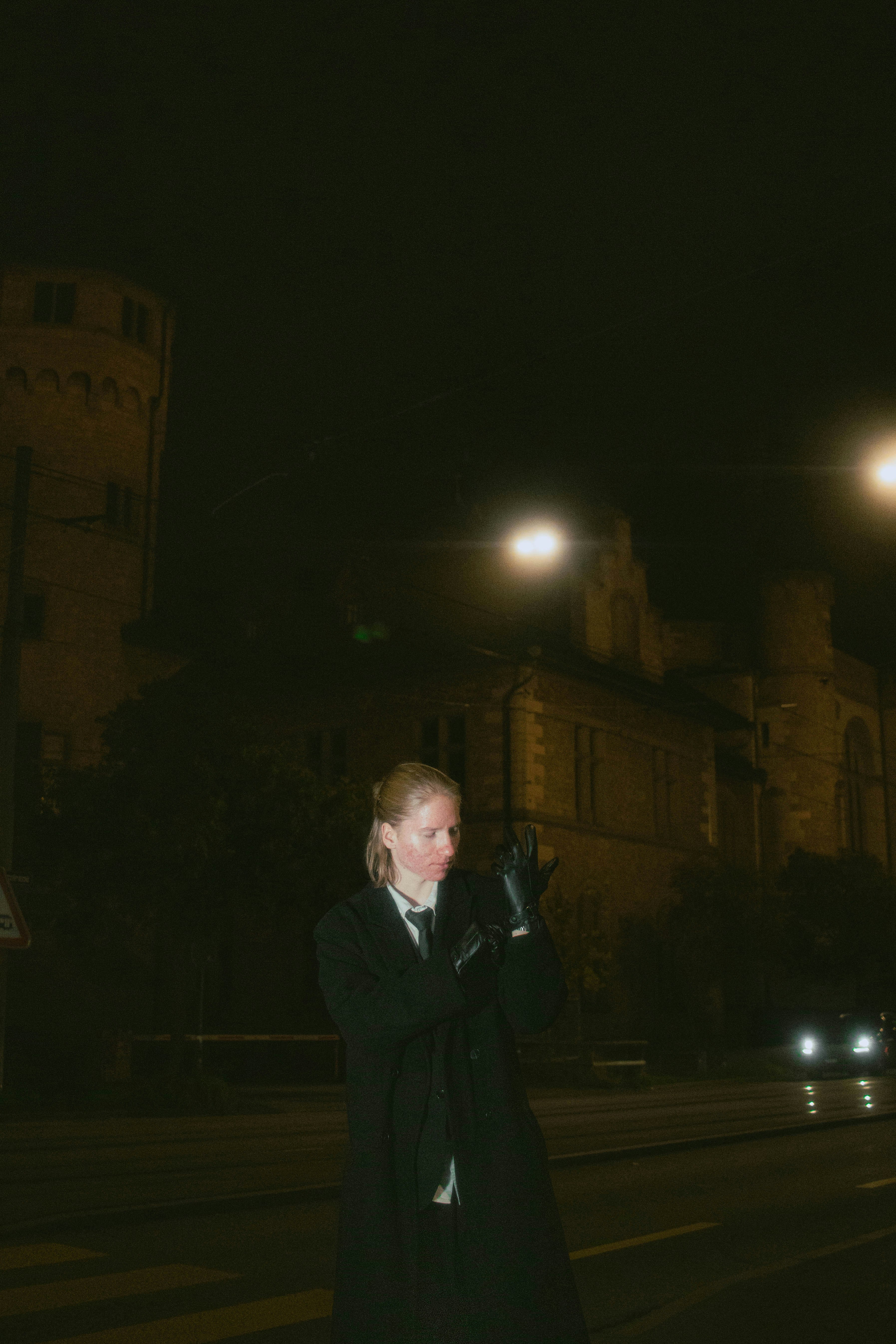 A woman in a long black coat standing on a street at night