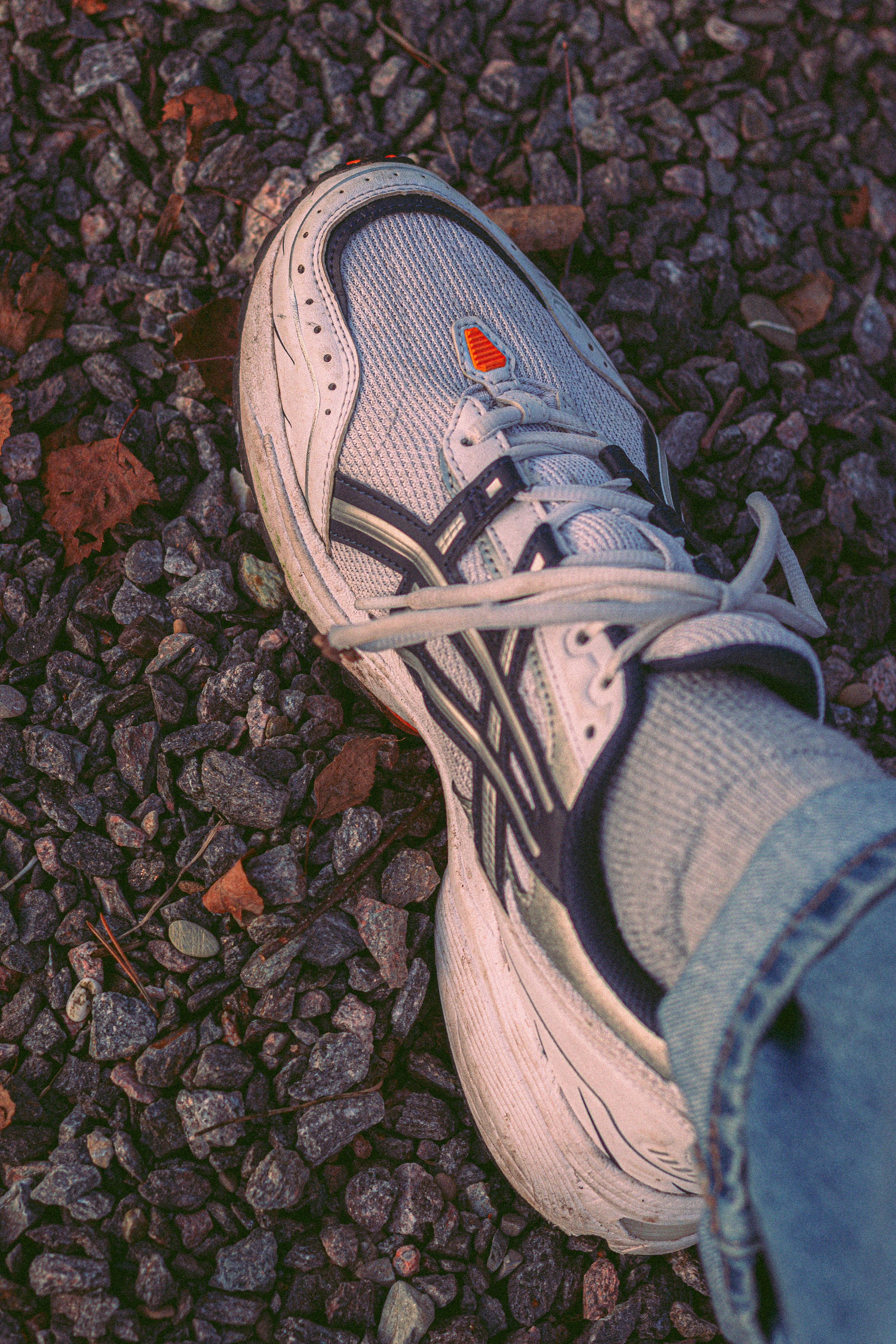 Gravelbound Run: A White Sneaker Resting on Pebble Bed in Warm Evening Light