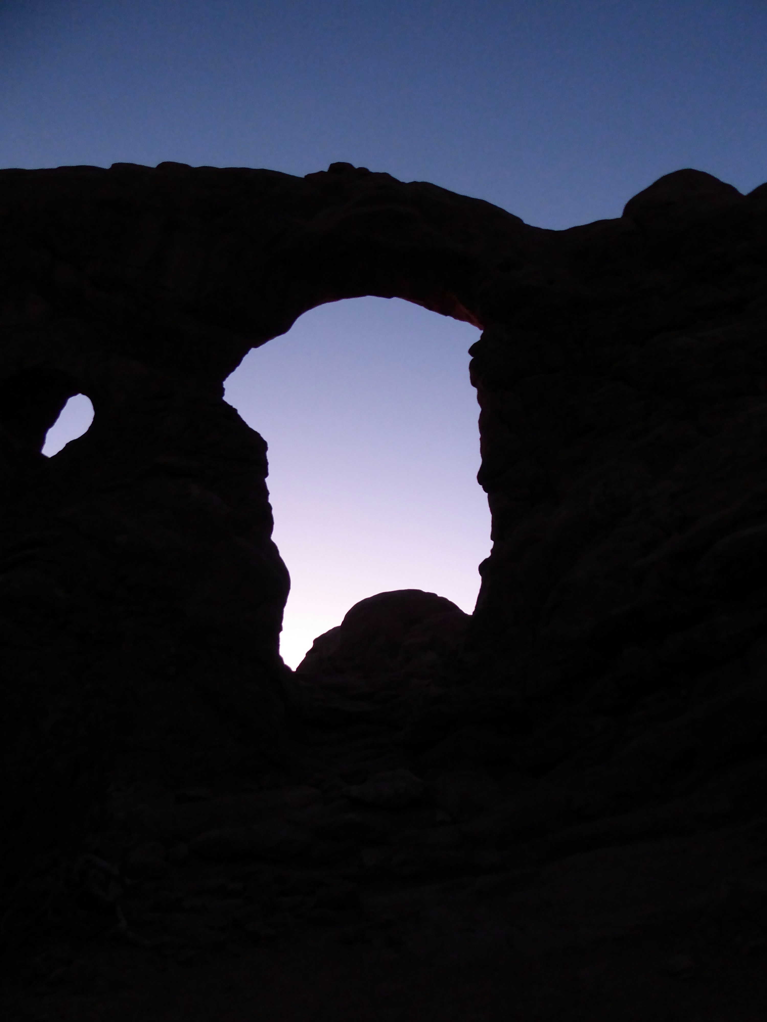 Silhouette of a rock arch framing a gradient twilight sky, forming a natural window.