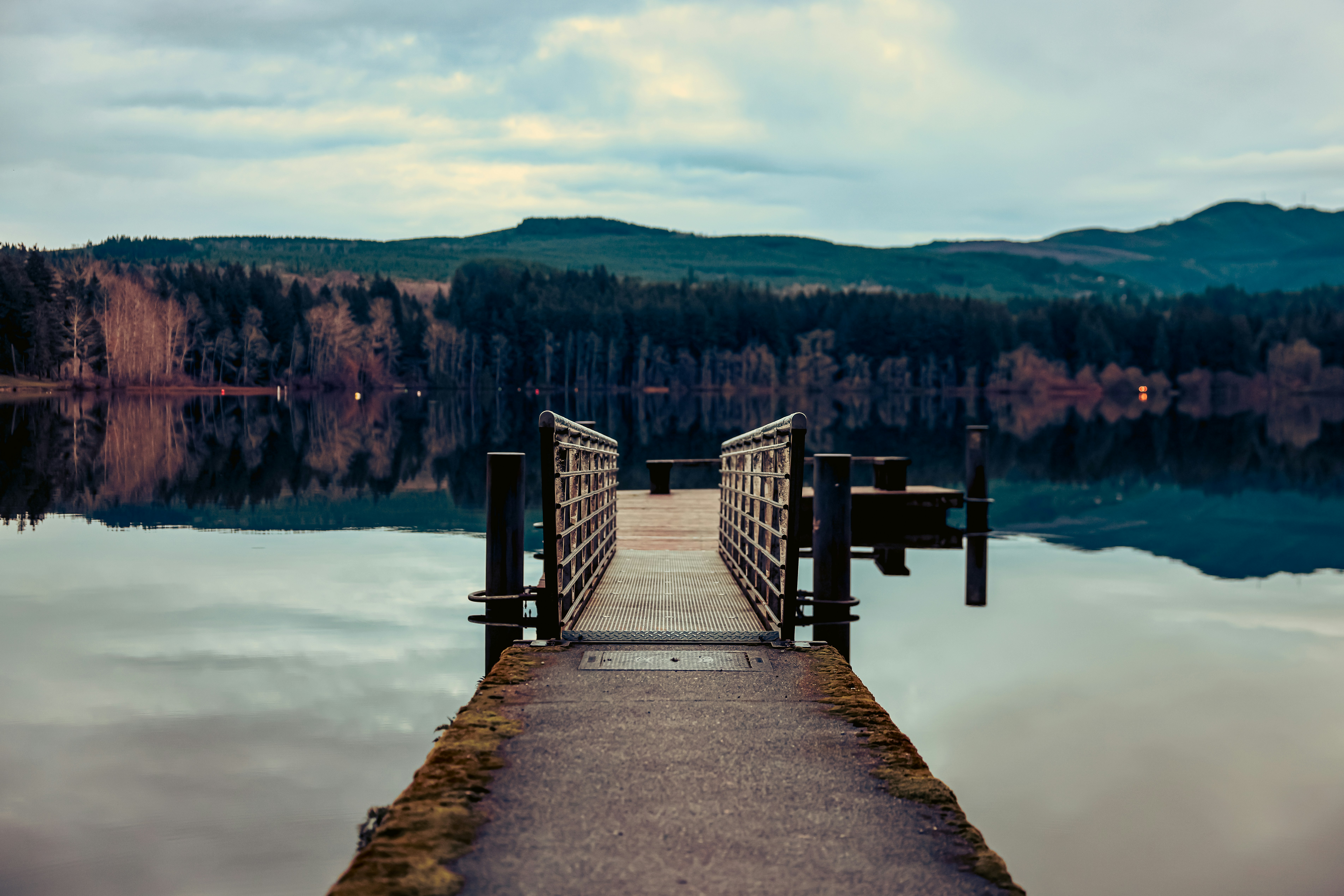Dock extending into Lake Padden with mirrored forested hills under an overcast sky.