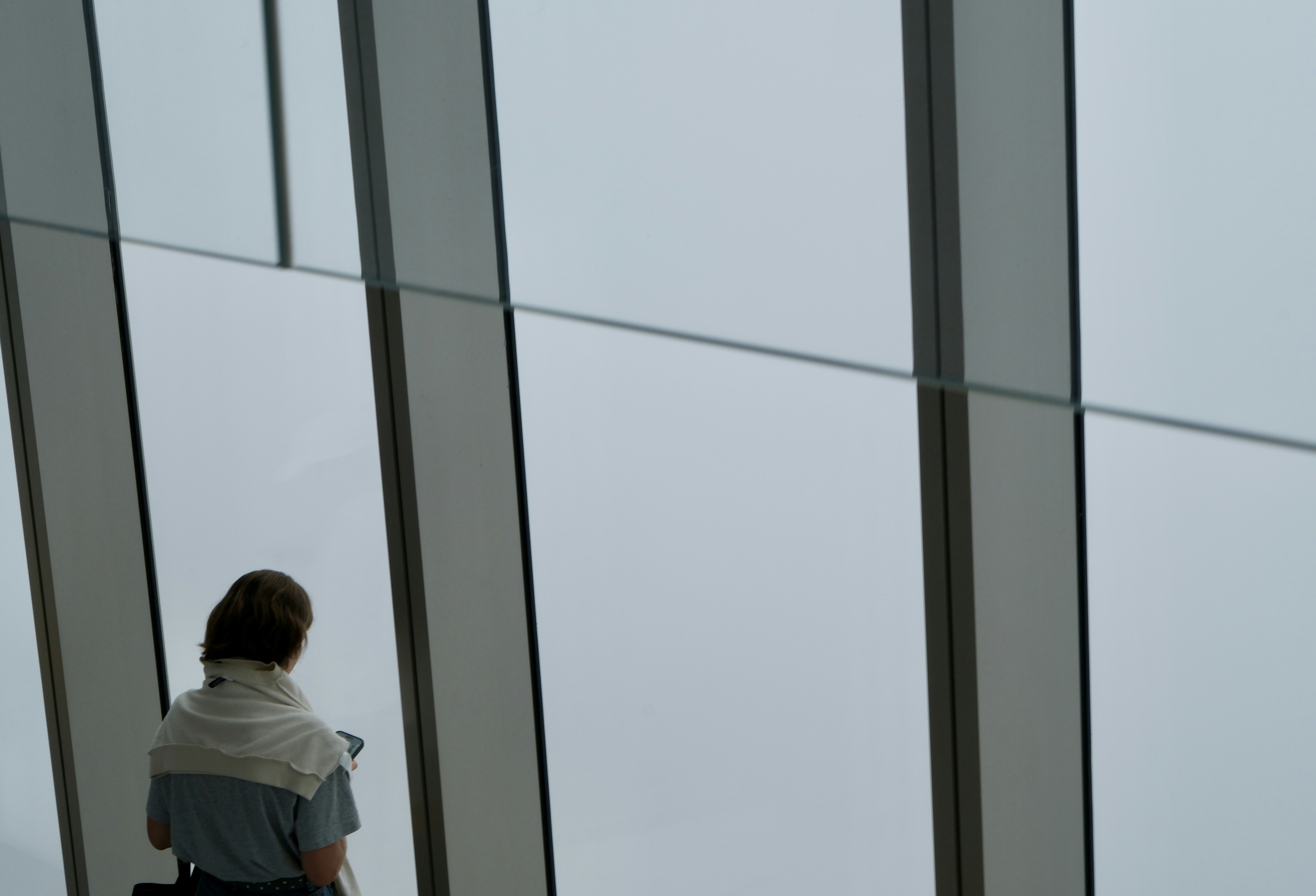 Person standing by large vertical windows with a foggy view outside.