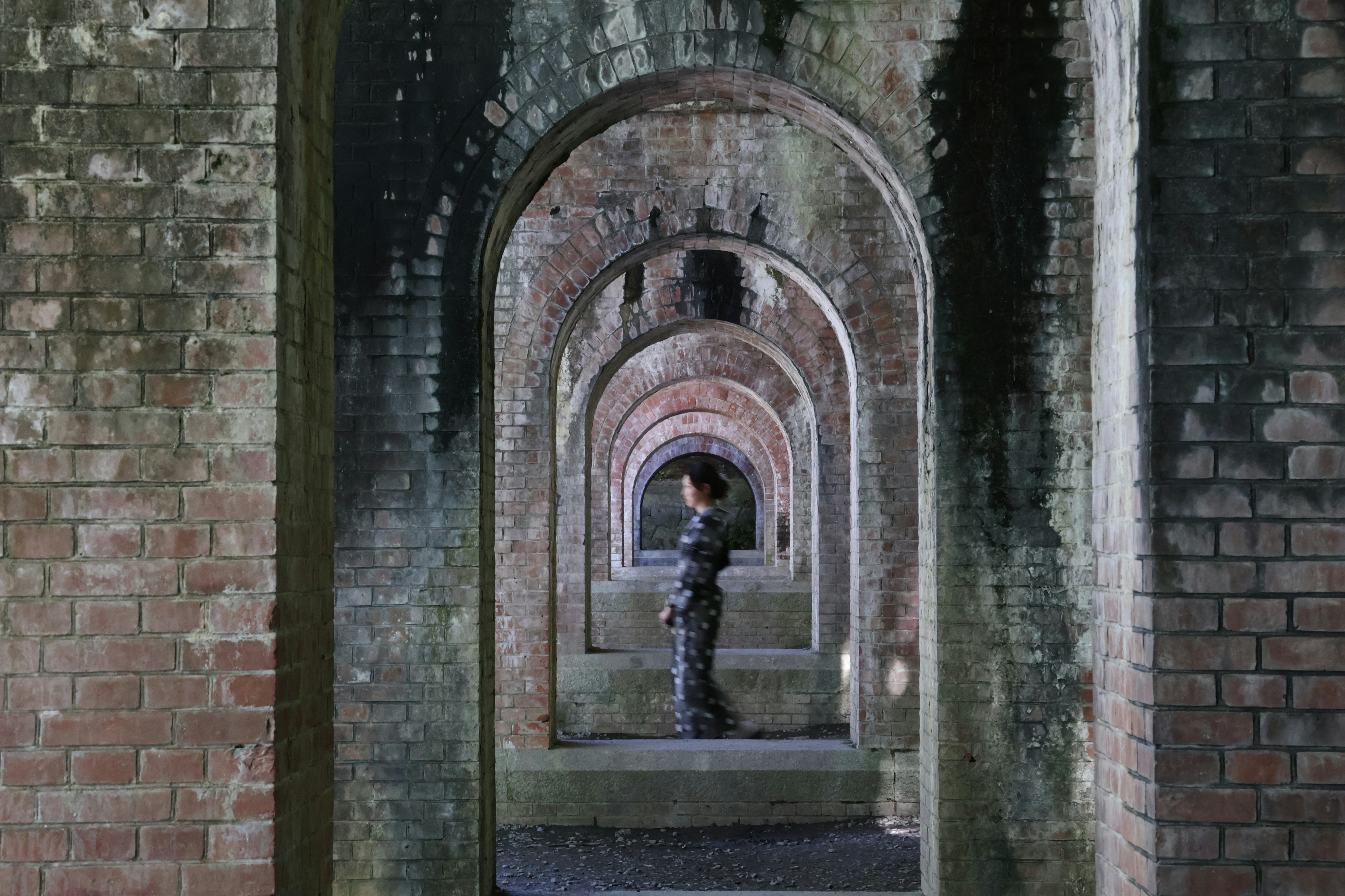 Vanishing Arches: a solitary figure in a brick tunnel
