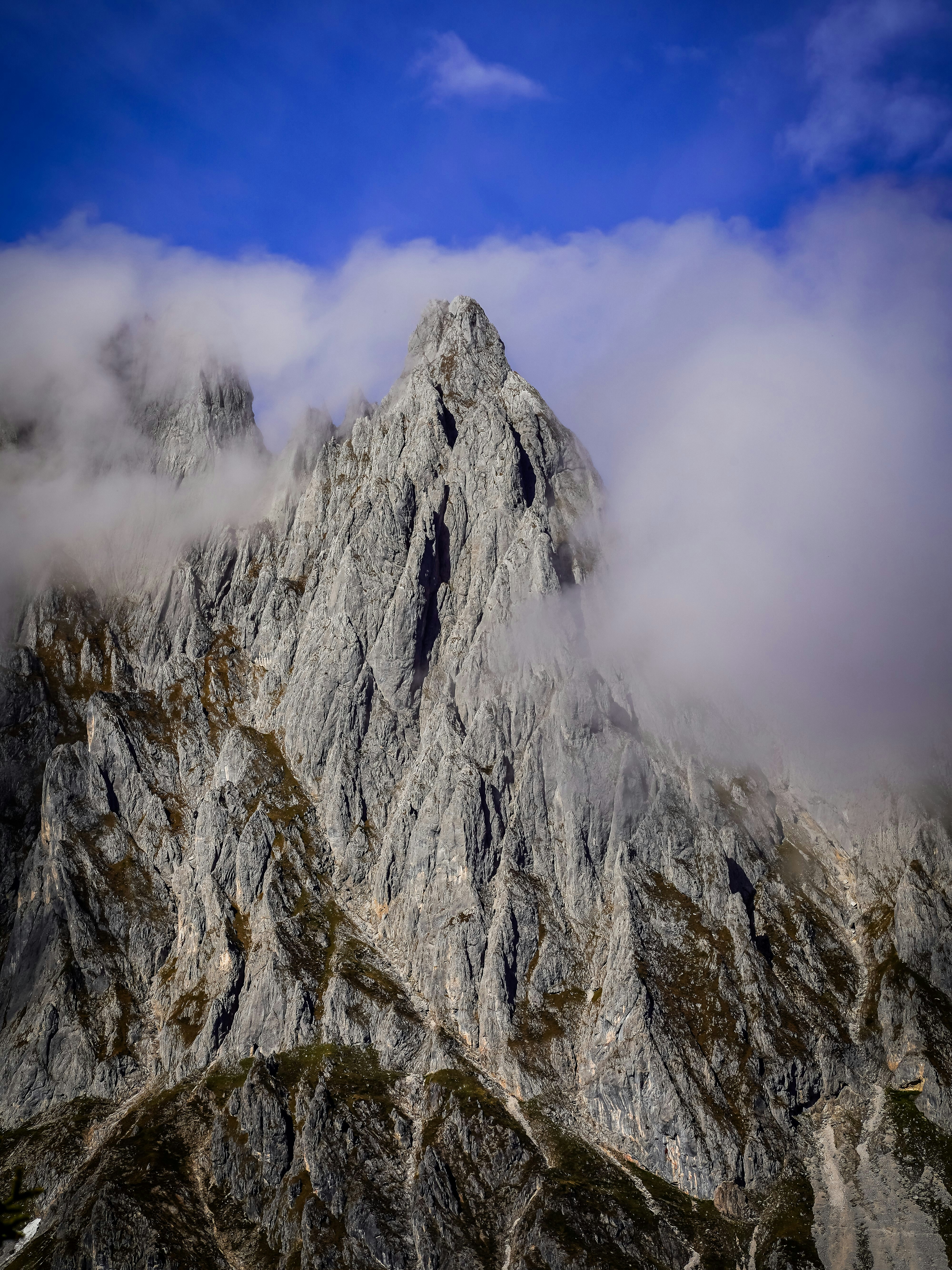 A very tall mountain covered in clouds under a blue sky photo – Free ...