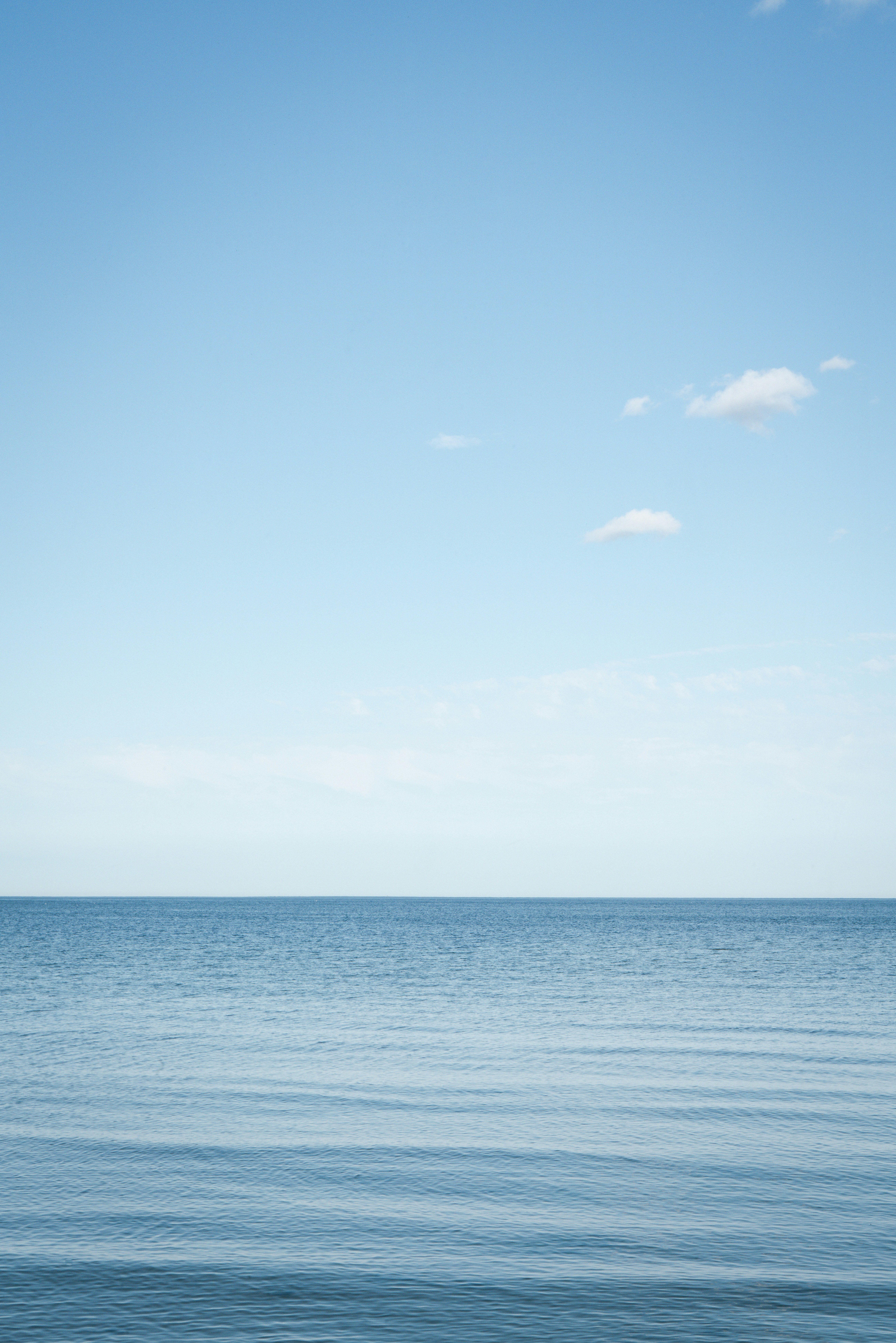 Vast ocean meeting a clear blue sky with gentle waves and soft clouds.