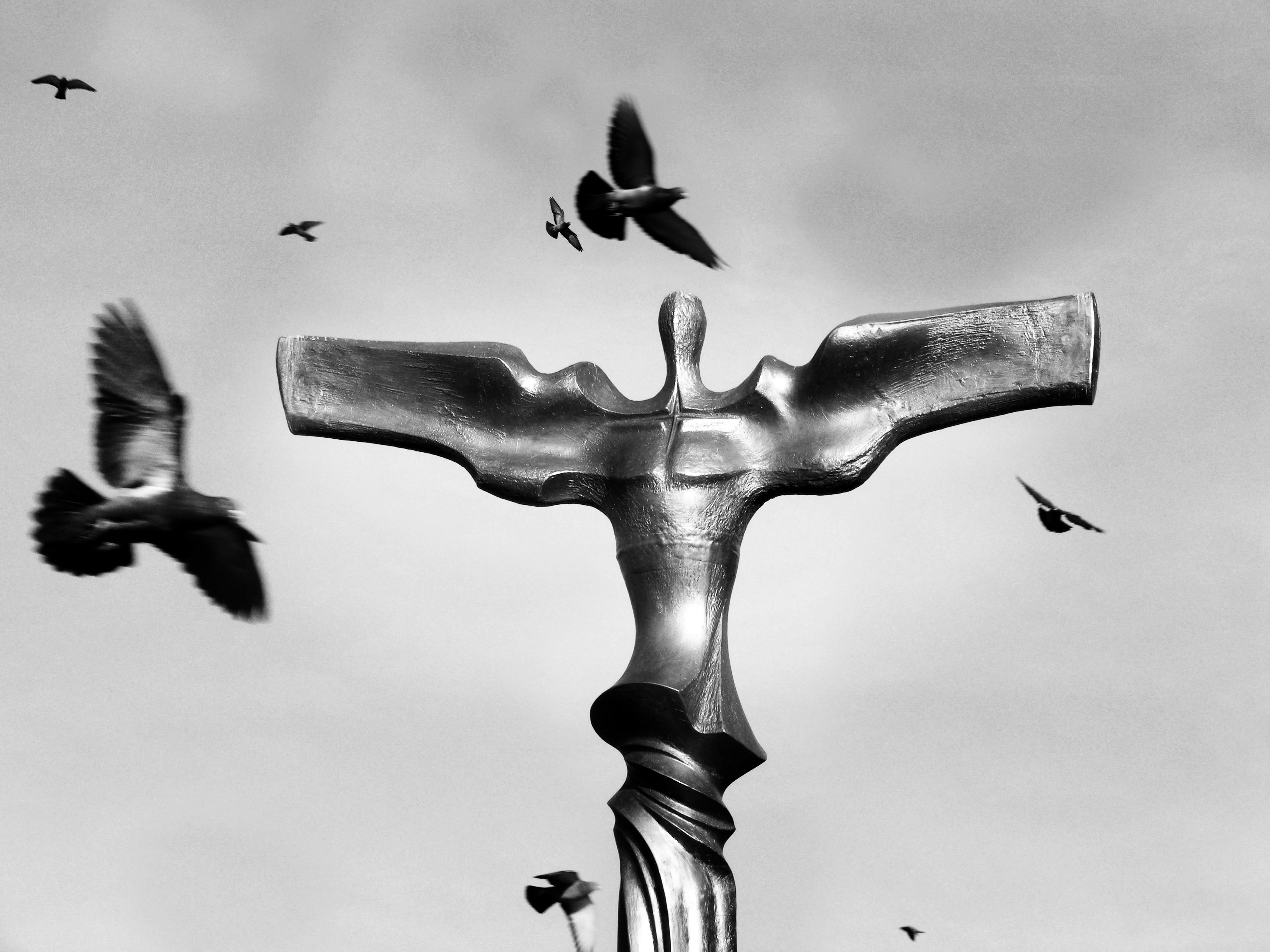 Iron Cross in Flight: A centered metal sculpture framed by wandering birds
